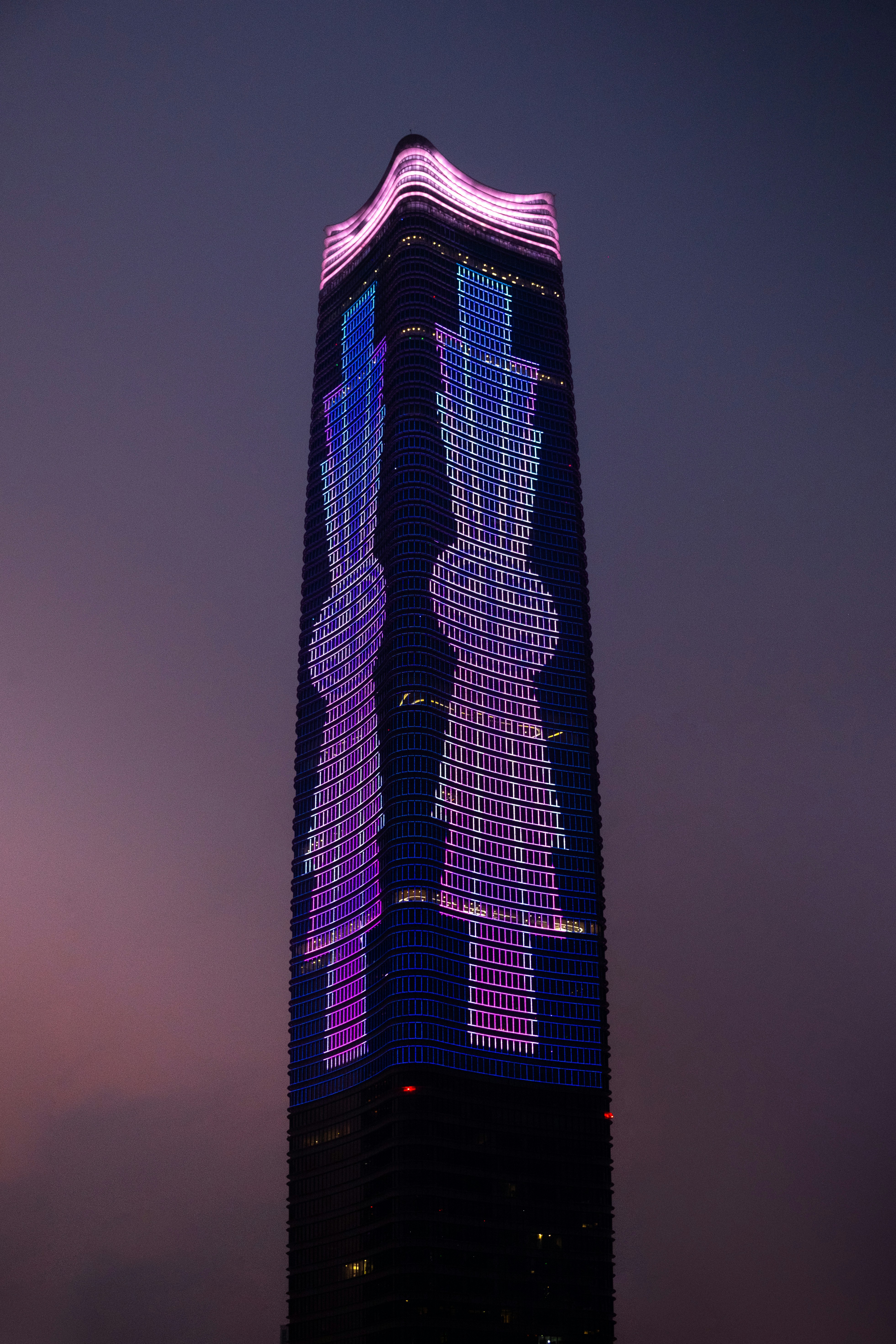 A skyscraper adorned with vibrant light displays, showcasing intricate patterns against a twilight sky.
