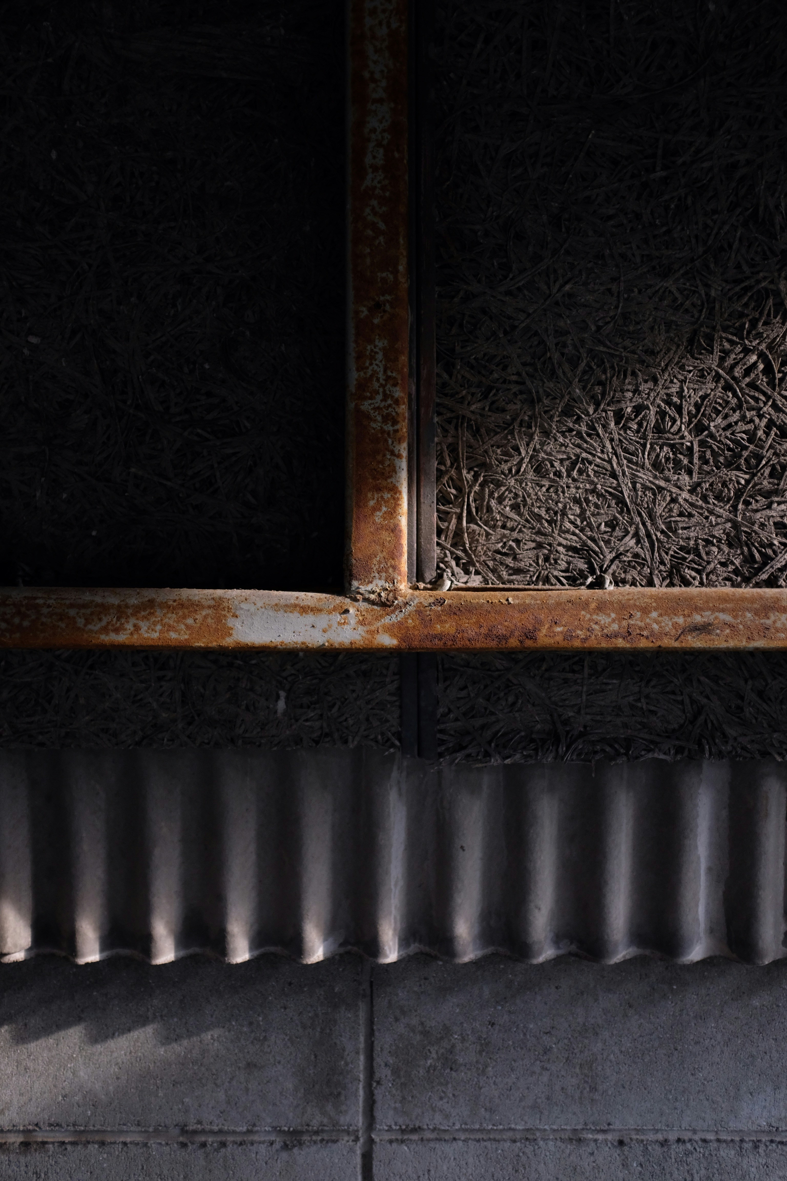Close-up of a rusted metal frame juxtaposed with textured surfaces and shadows, highlighting the interplay of light and material.