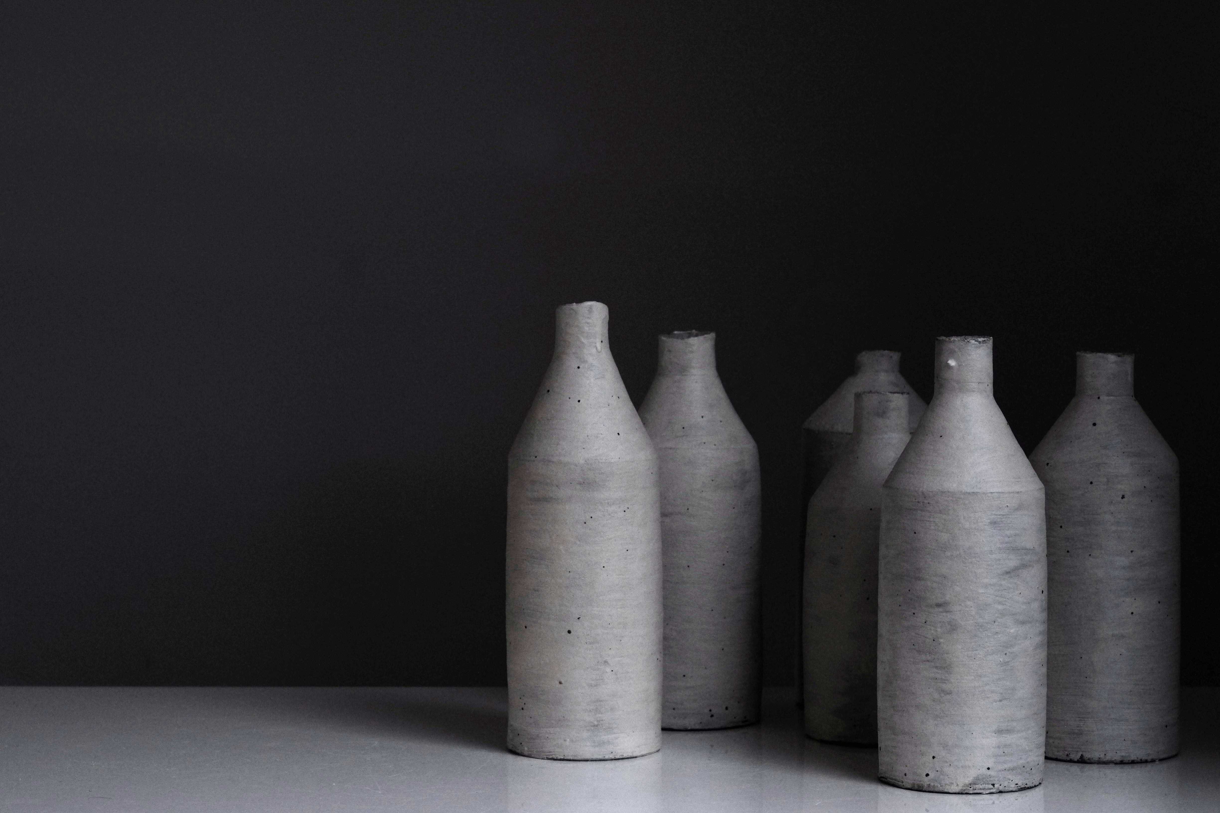 A collection of minimalist concrete vases arranged on a white surface against a dark background, emphasizing their unique shapes and textures.