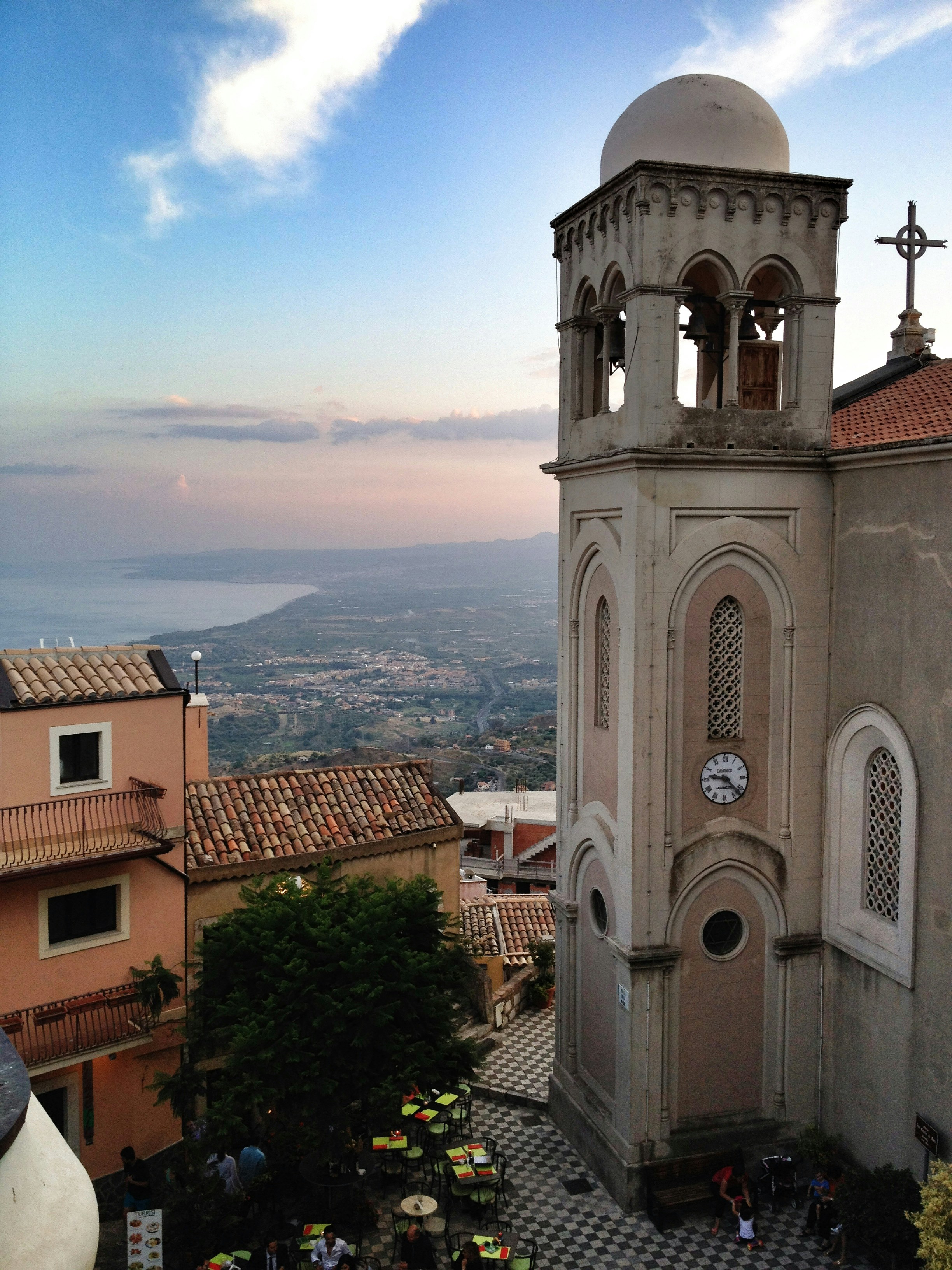 Charming clock tower stands amidst terracotta rooftops, overlooking a picturesque coastal landscape at dusk.