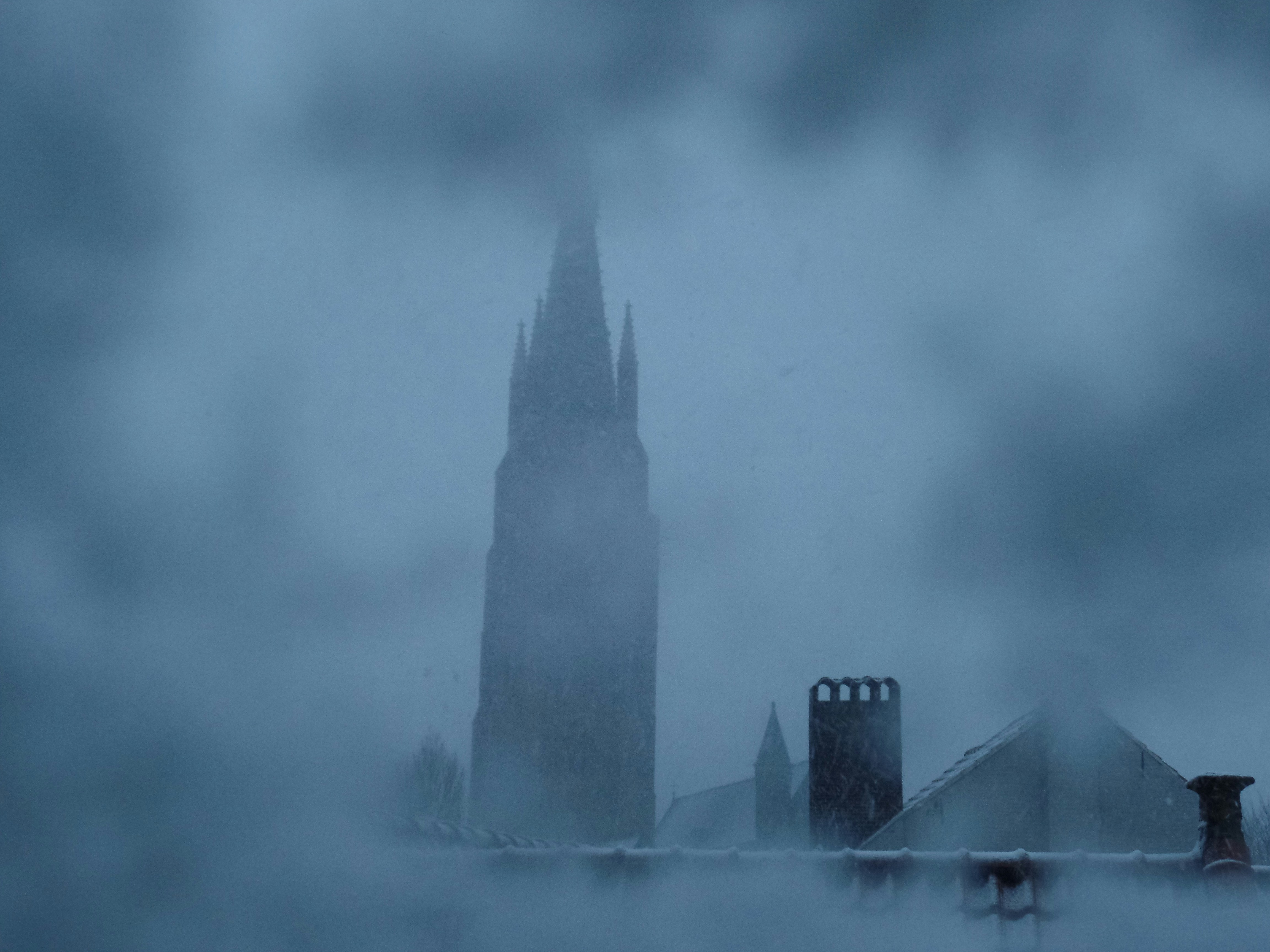Silhouetted gothic spire rising through dense fog with chimneys in foreground.