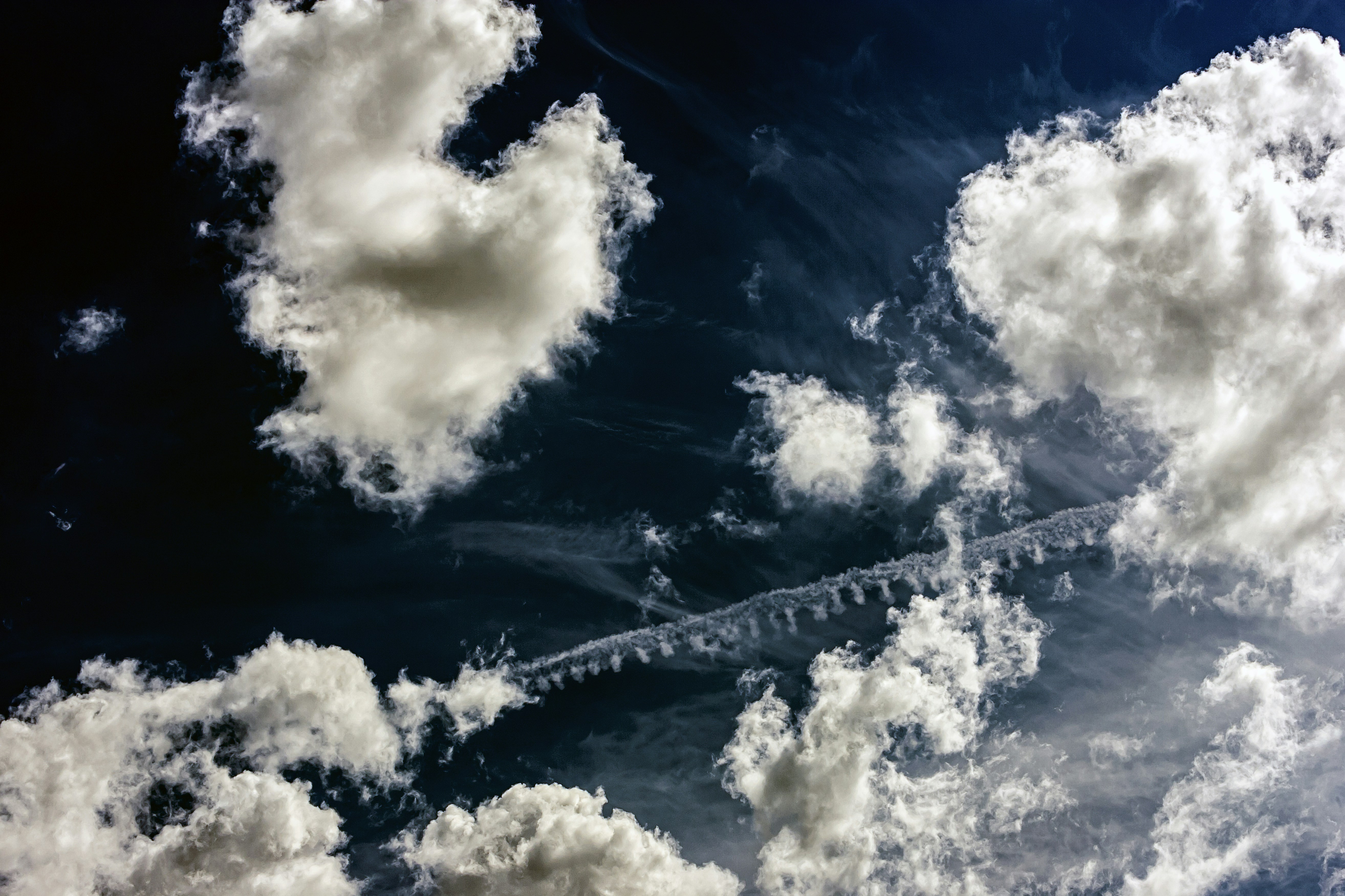Fluffy clouds drift across a deep blue sky, interspersed with a faint contrail stretching horizontally. The scene captures the serene beauty of a clear day.