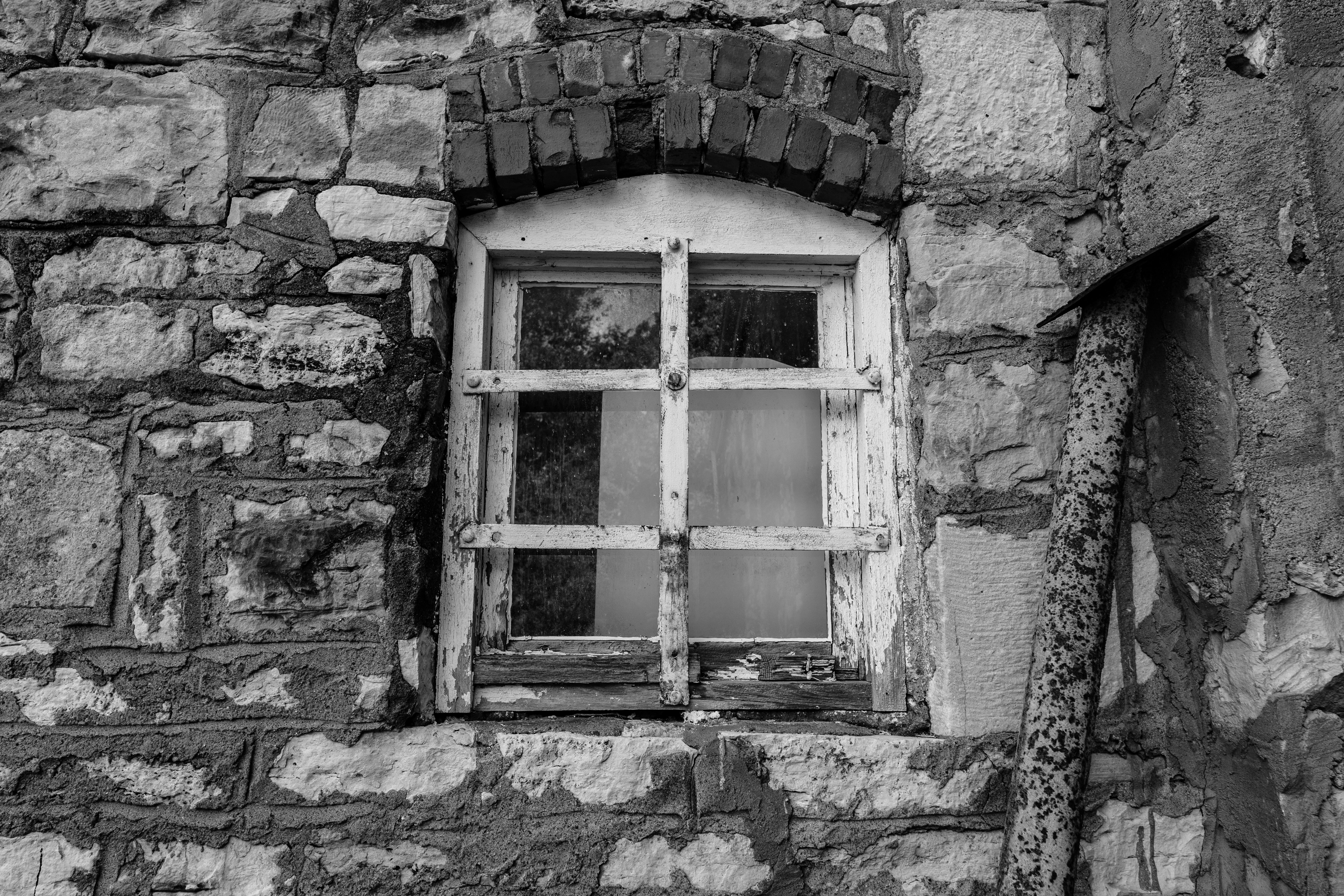 Weathered window set in a rustic stone wall, showcasing the textures of decay and history. The scene is presented in black and white, enhancing its timeless quality.