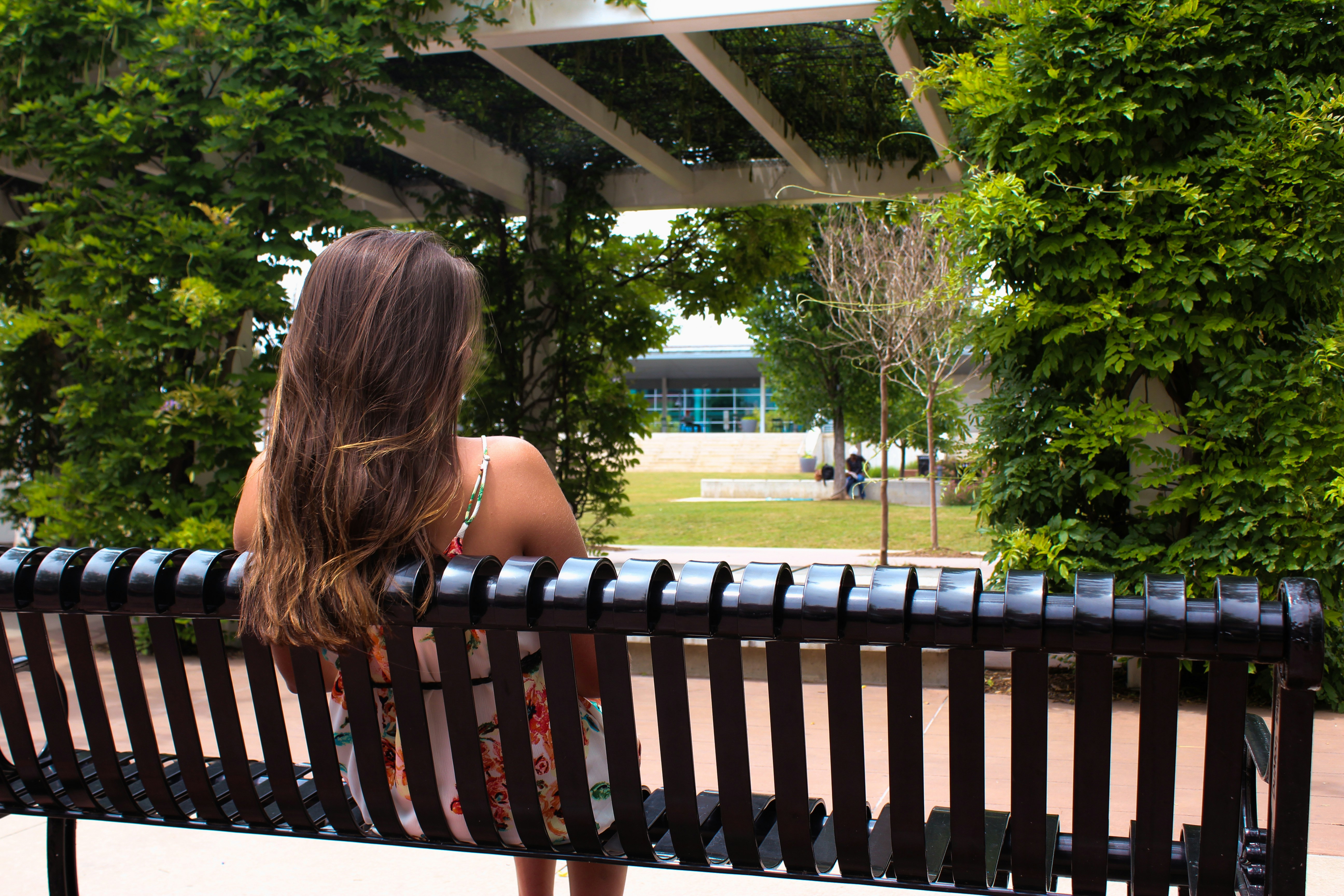 Person sitting on a metal bench surrounded by lush greenery and garden structures.