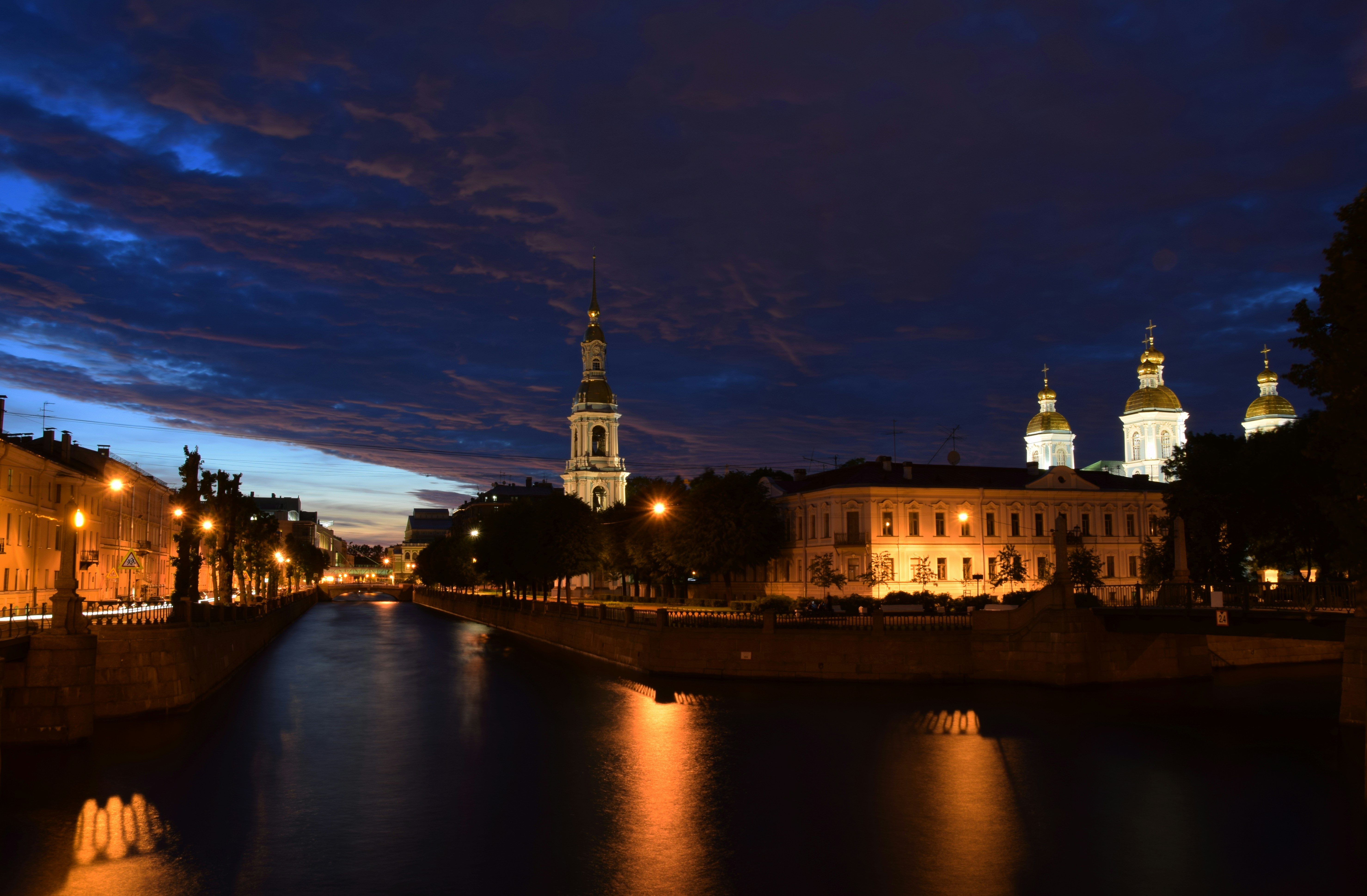 Historic buildings illuminated along a riverbank under a twilight sky.
