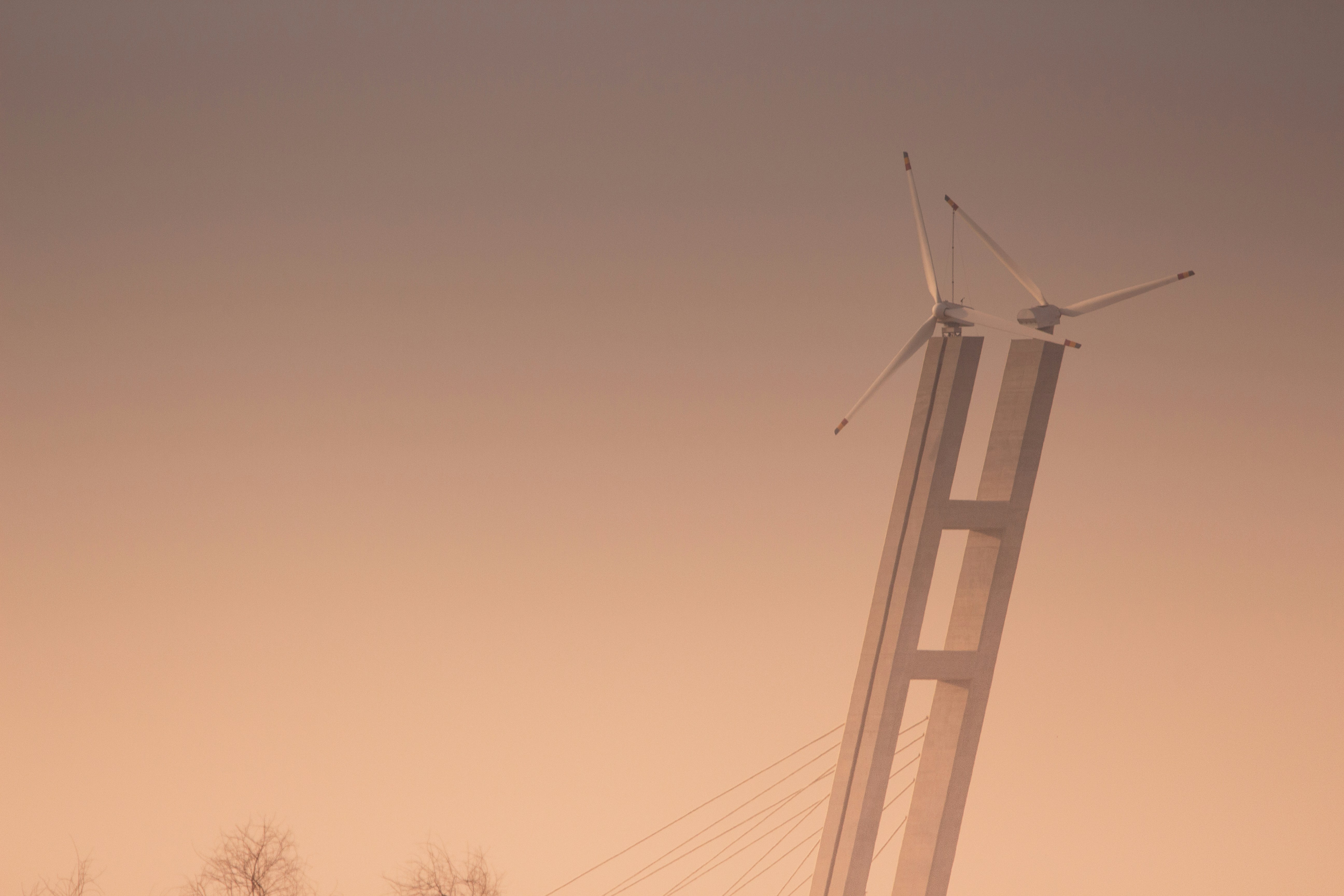 A leaning wind turbine stands against a soft, pastel sky, highlighting the intersection of nature and technology. The silhouette contrasts with the gentle hues of dawn.