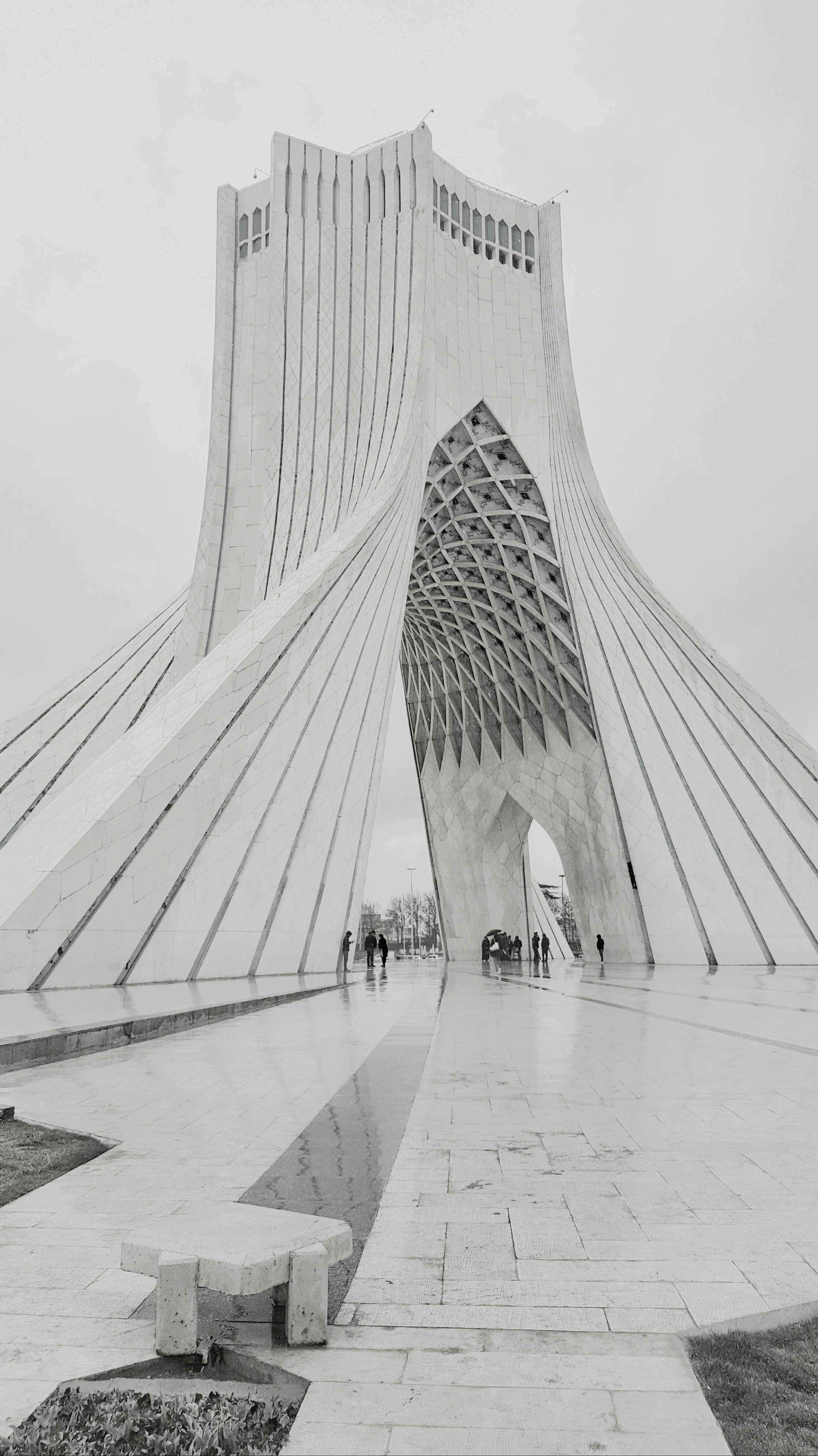 A striking view of a modern architectural structure featuring sweeping lines and intricate geometric patterns. The scene captures visitors exploring the space beneath the towering design.