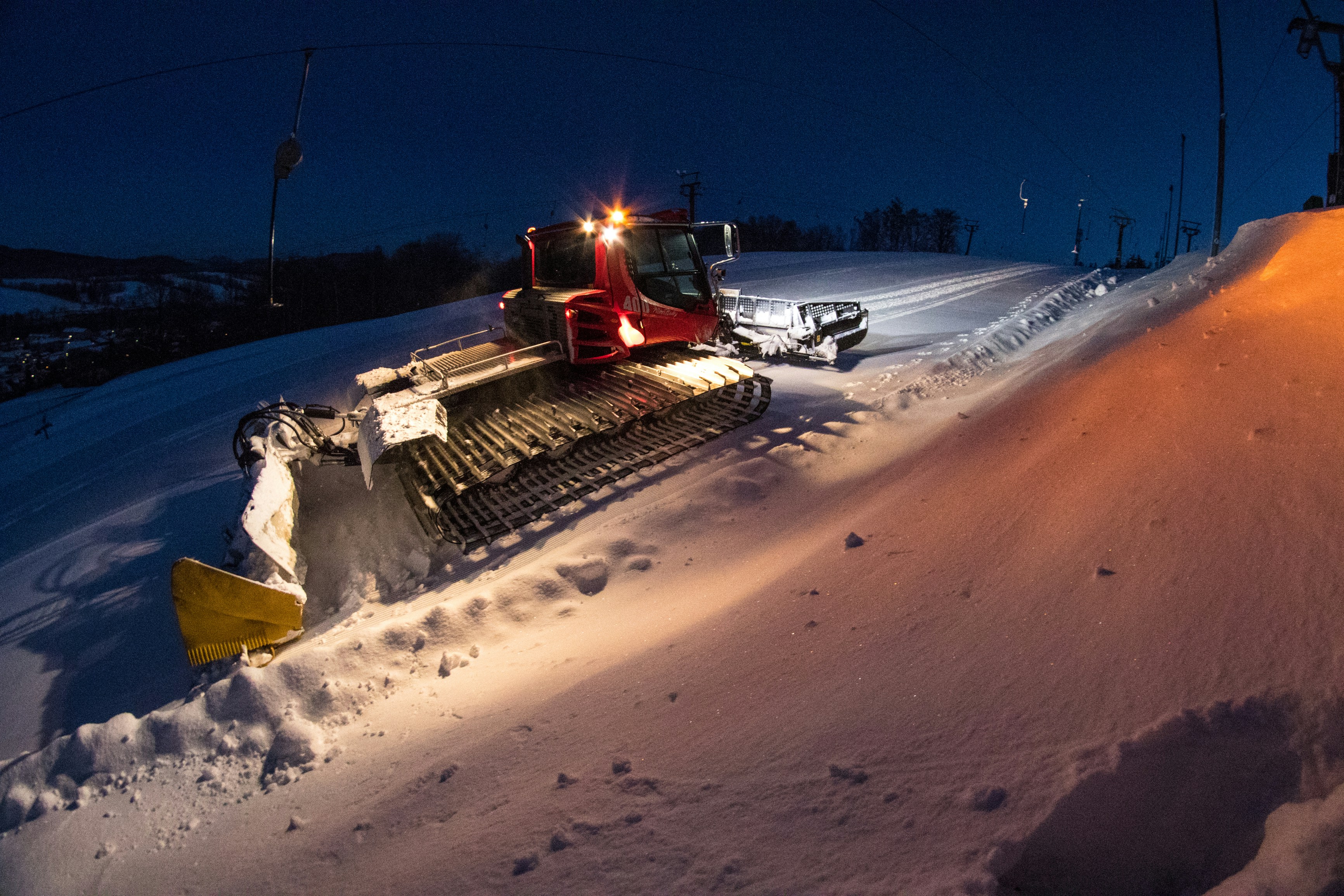 Drill on Snowfront: A Snowcat Streak Under a Dark Alpine Sky