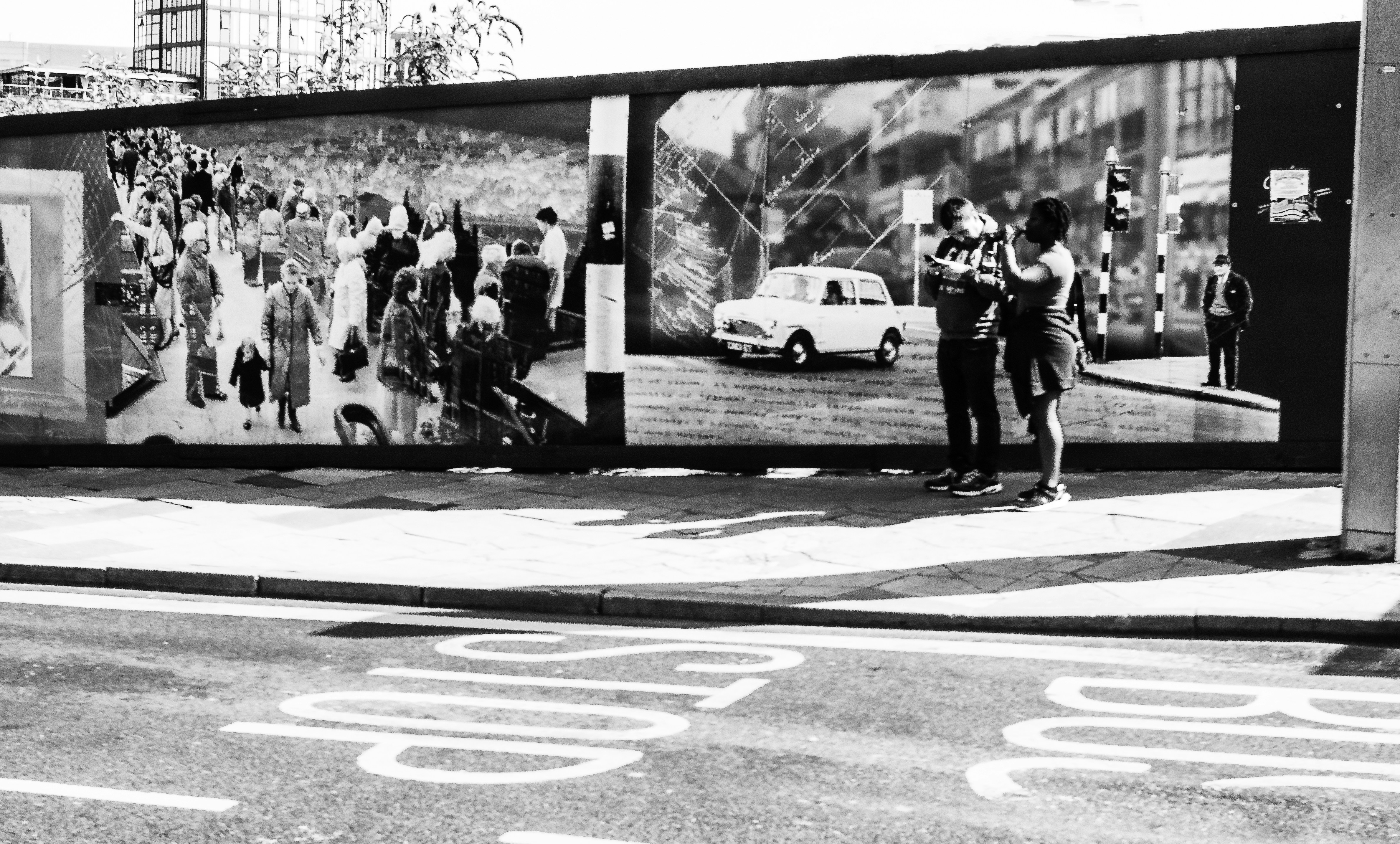 Transit Corridor: A Bus Stop Ad Wall Framed by Pedestrians and a Classic Car