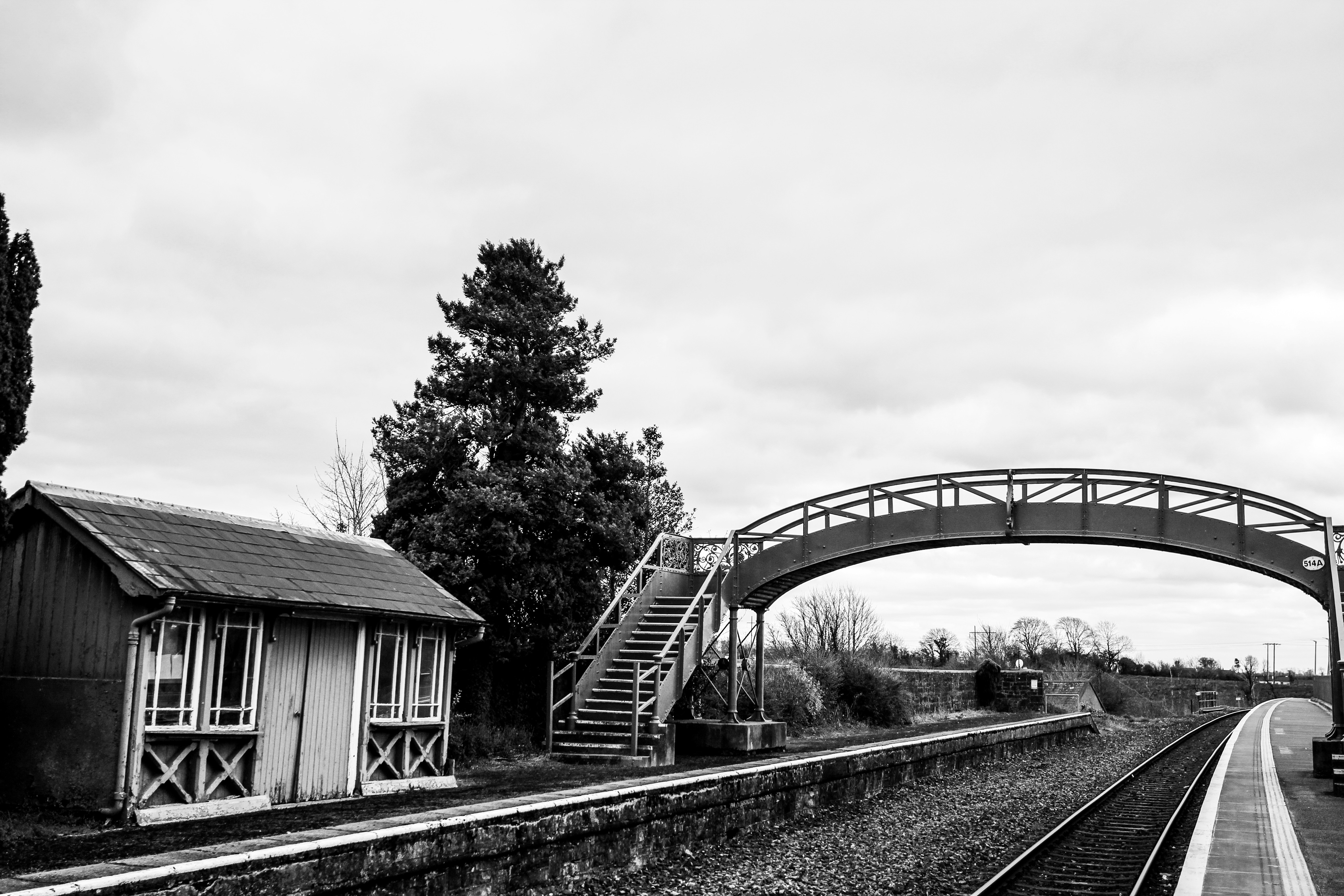 Abandoned train station with a vintage wooden building and an ornate footbridge, set against a moody sky. The scene evokes nostalgia for a bygone era.