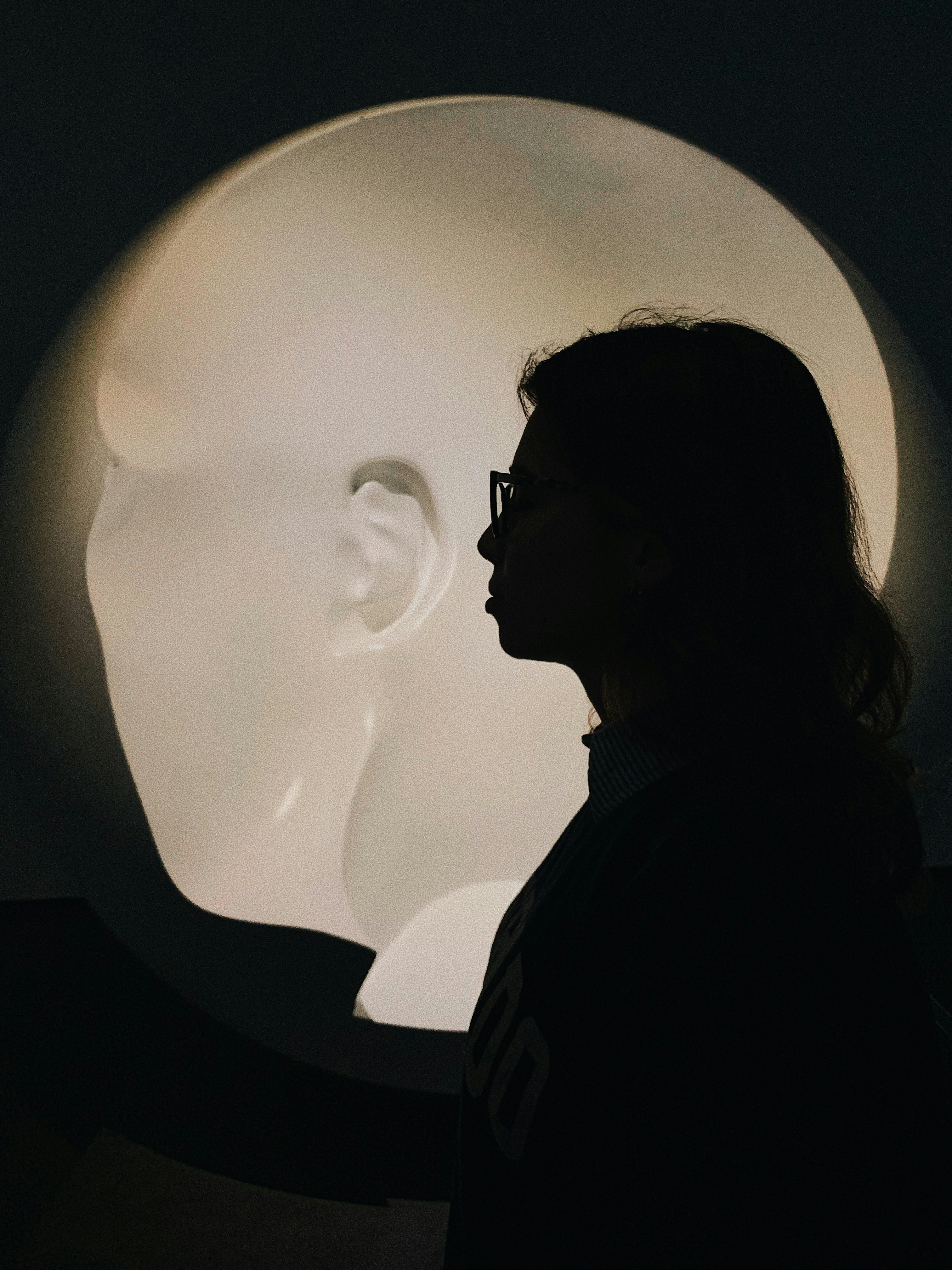 Shadowed silhouette against a luminous oversized head sculpture