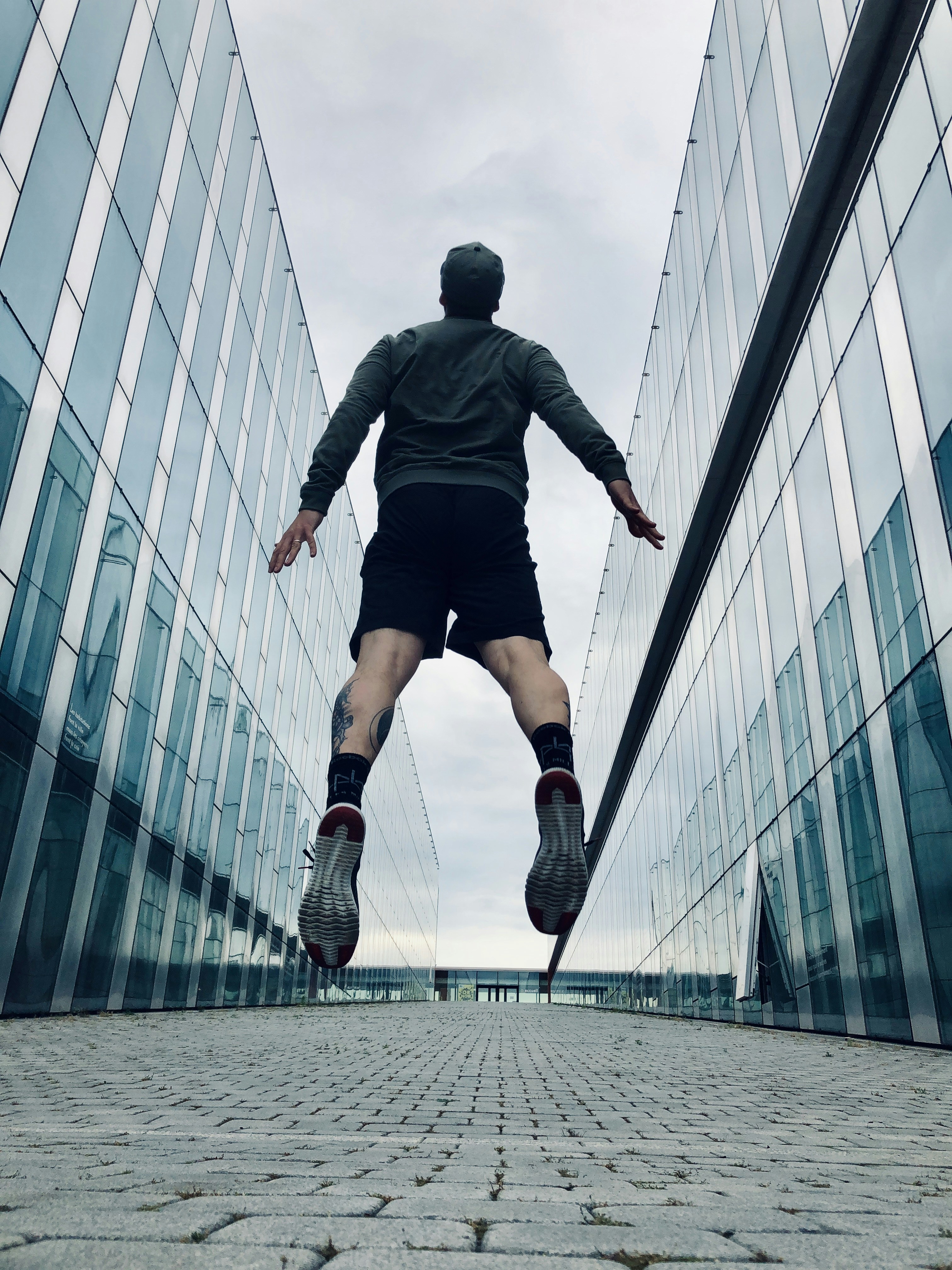 Person in mid-air leap between two mirrored glass buildings under a cloudy sky.