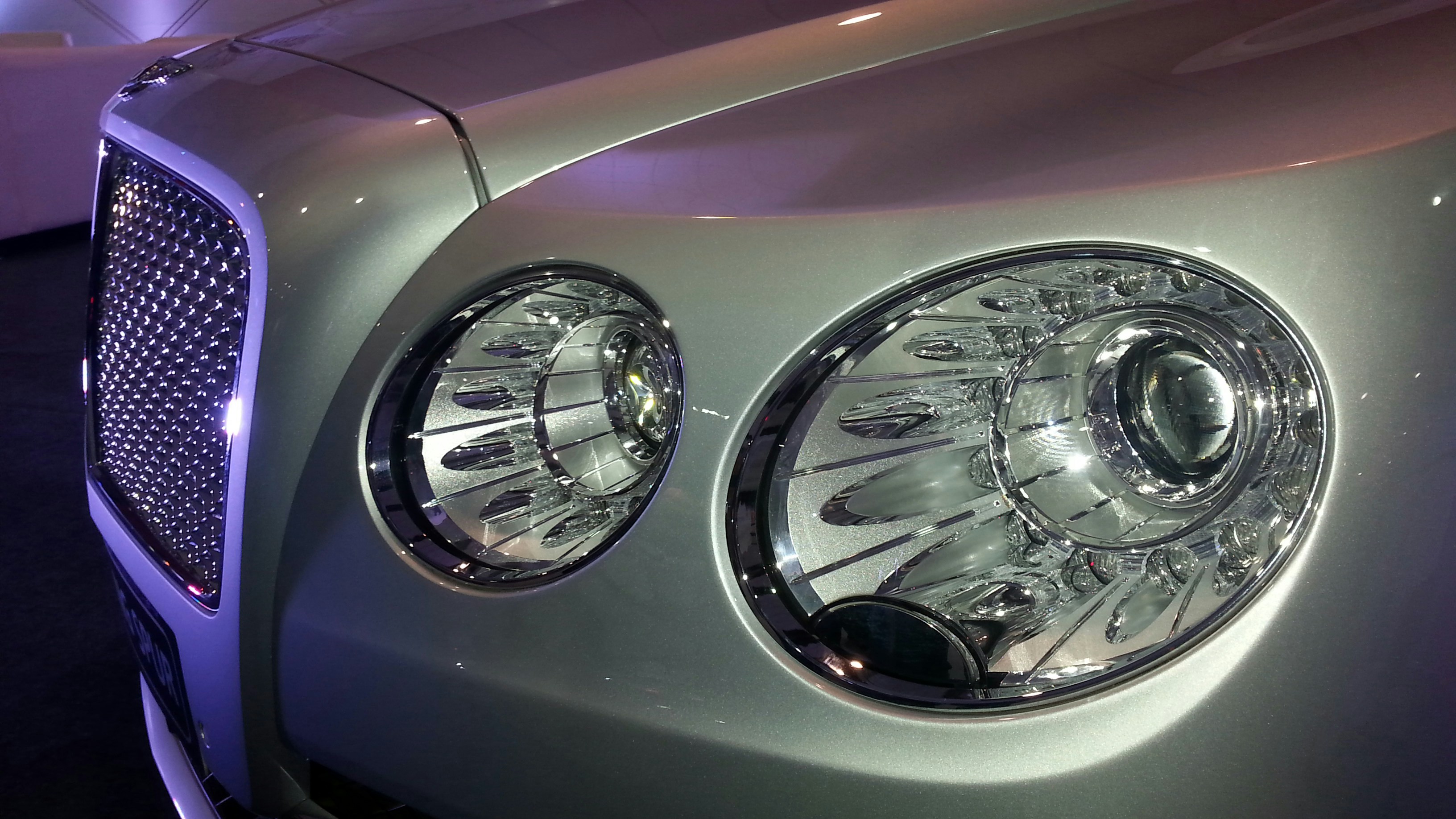 Close-up of a luxury car's intricate headlight design beneath soft ambient lighting.