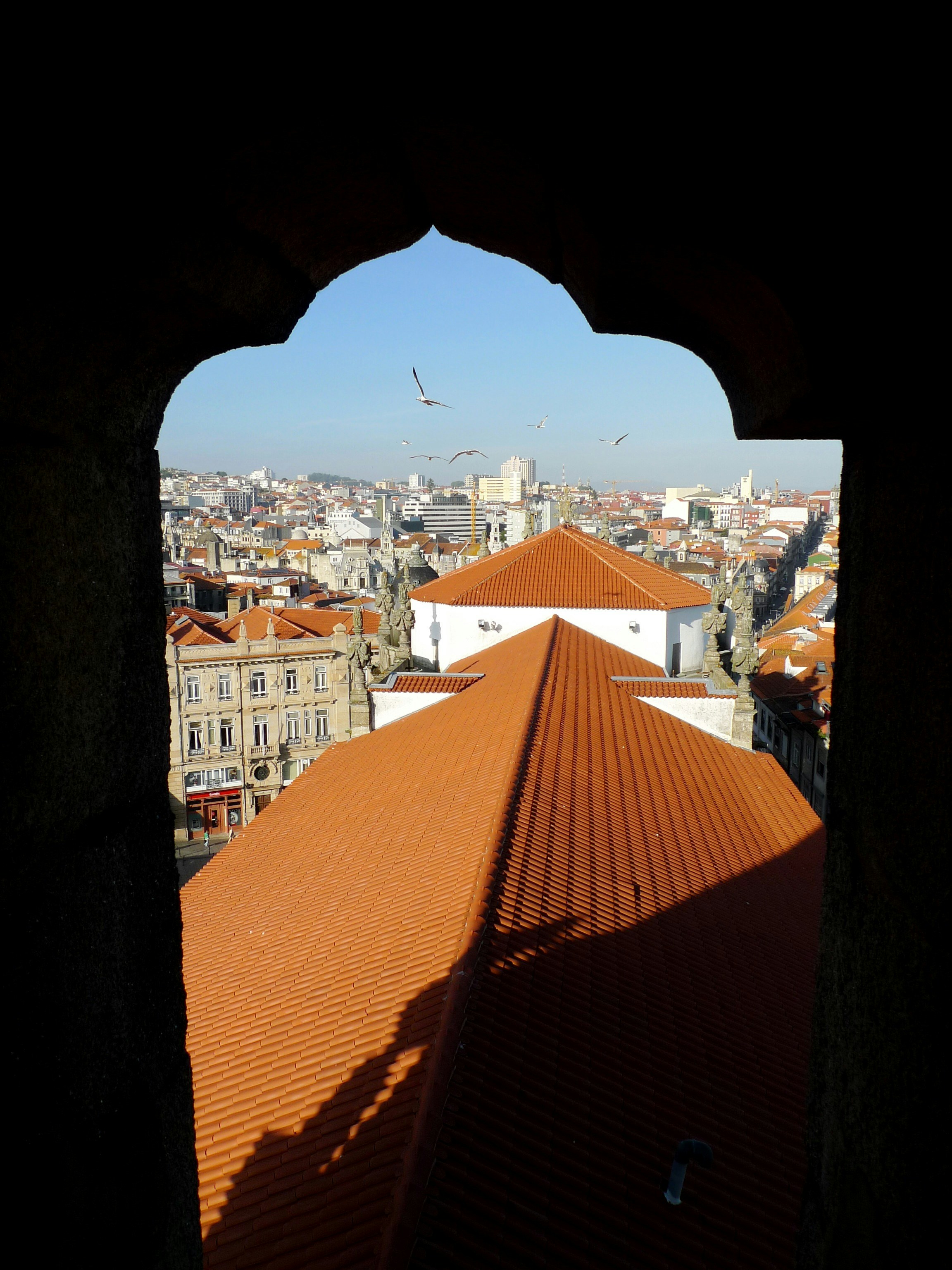View of a cityscape framed by an ornate stone arch, showcasing terracotta roofs and distant buildings under a clear sky.