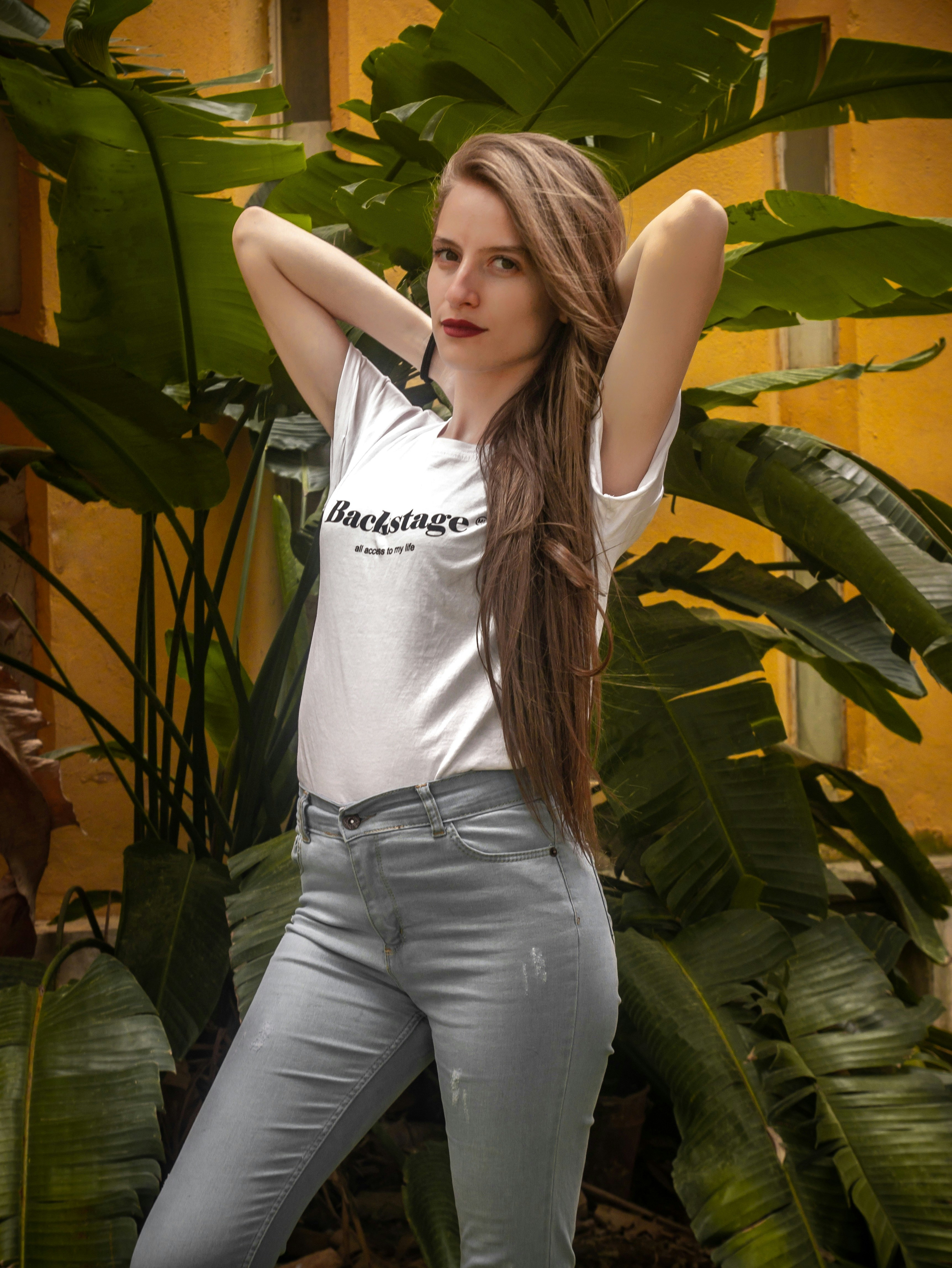 Model posed against lush green foliage, showcasing a stylish outfit with a playful expression. The vibrant background enhances the overall aesthetic.