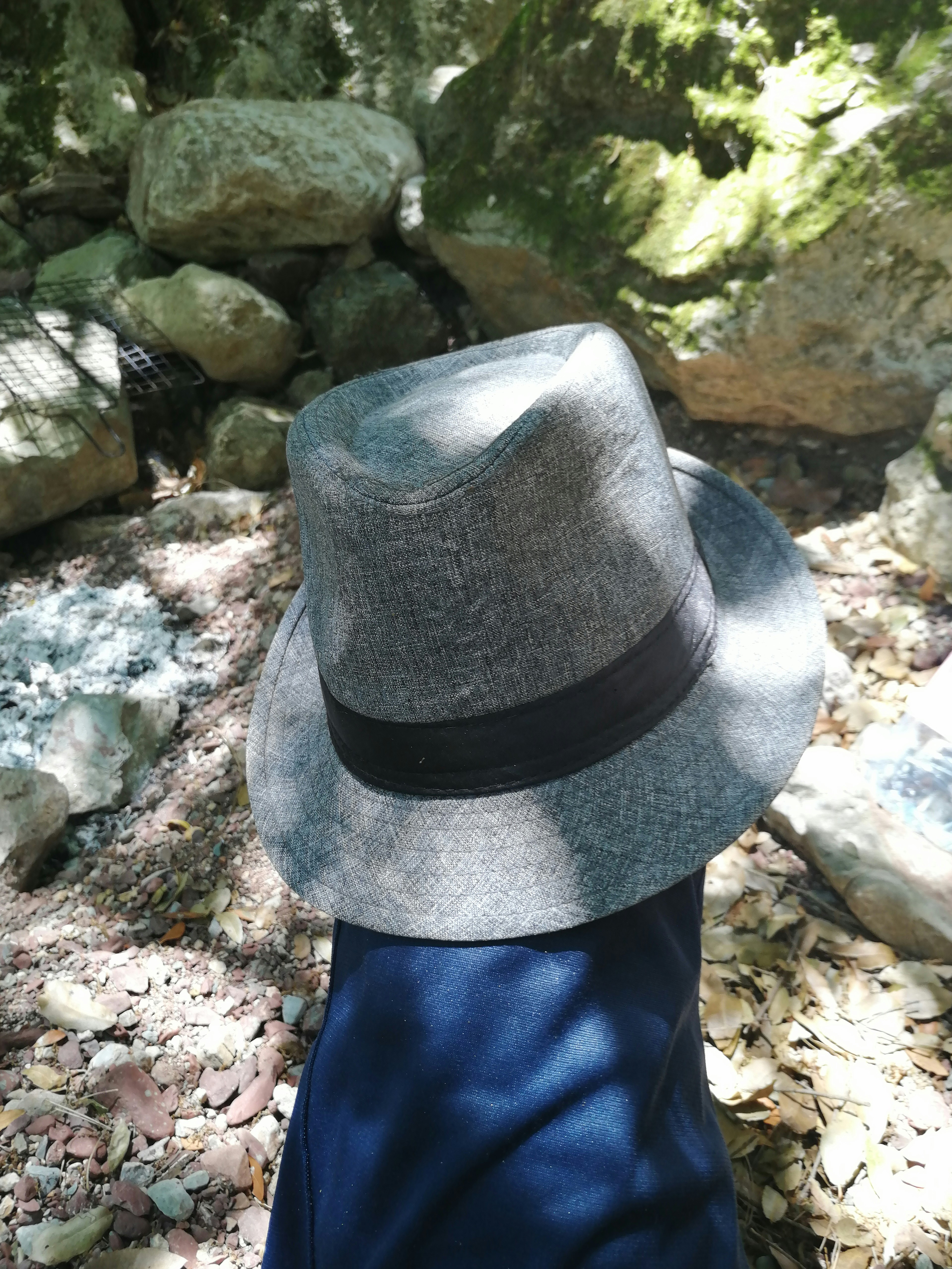 A gray fedora resting on a person's lap amidst a rocky landscape, dappled with sunlight and shadows.