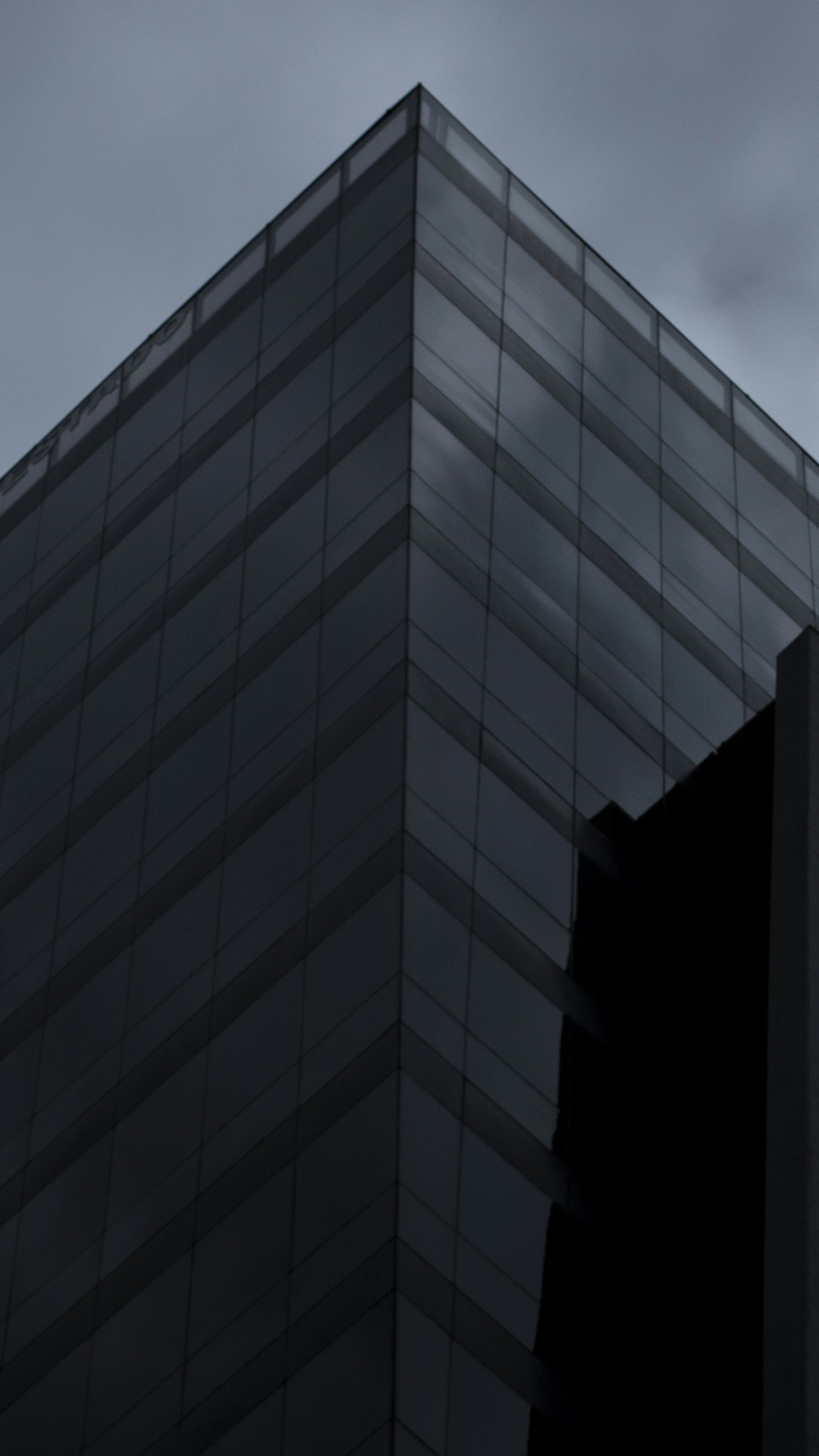 Angular glass structure reflecting the overcast sky, showcasing a modern architectural design.