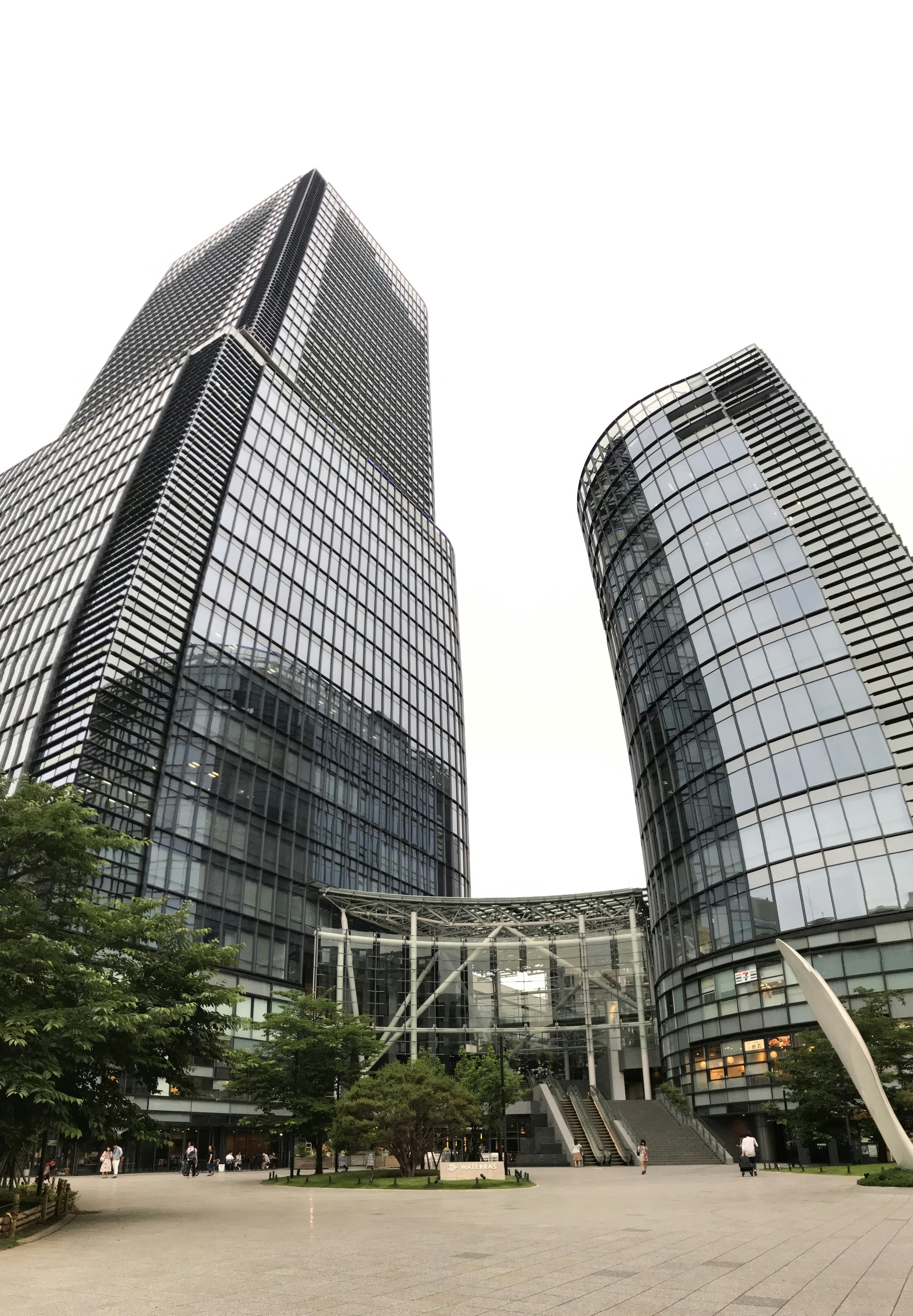 Modern skyscrapers with striking glass facades rise above a landscaped plaza, showcasing contemporary architectural design.