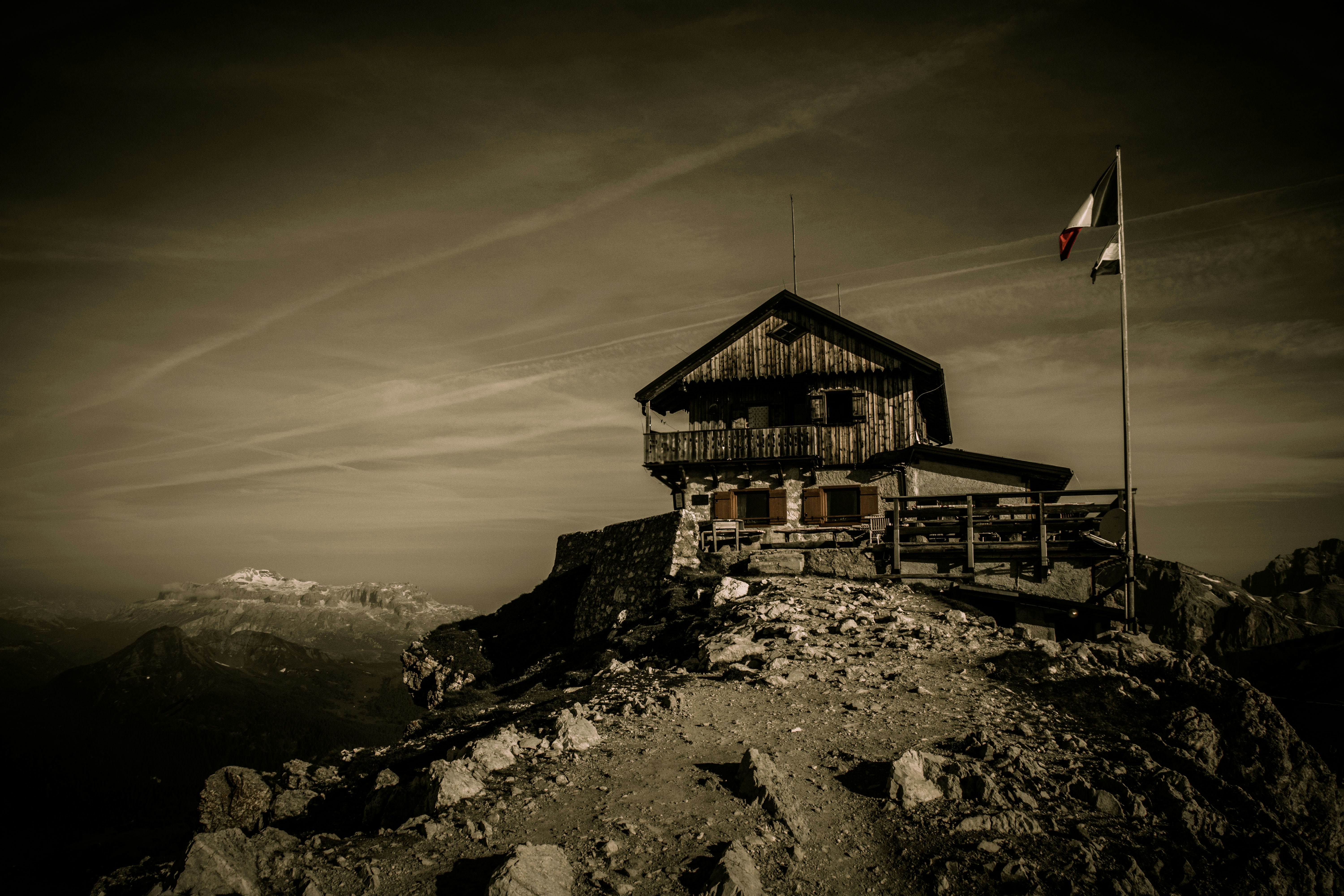 Rustic mountain hut perched on a rocky ridge, with flags fluttering in the breeze against a backdrop of distant peaks.