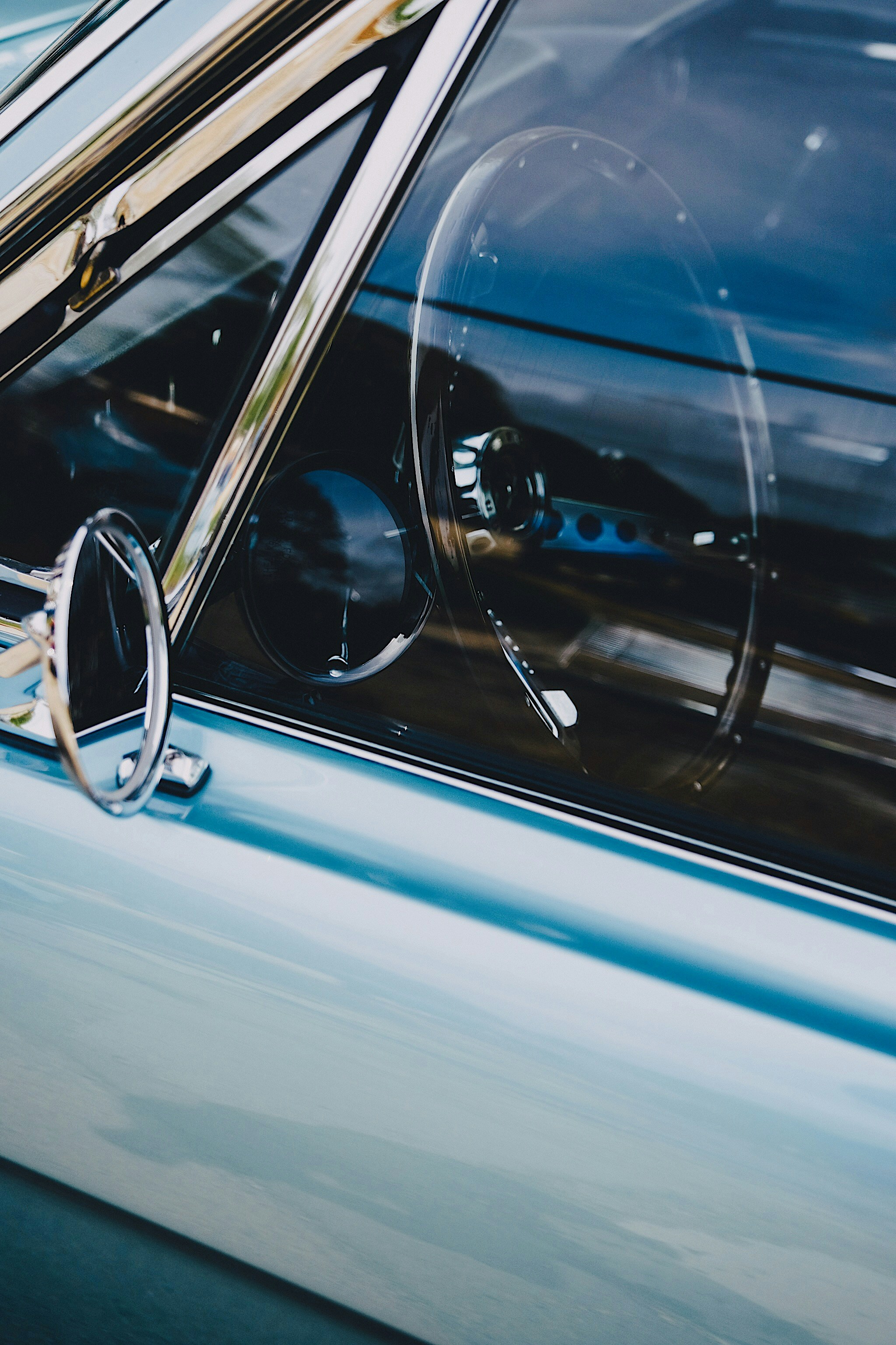 Close-up of a vintage car's interior, showcasing the steering wheel and chrome details through the window. The interplay of light and reflections adds depth.