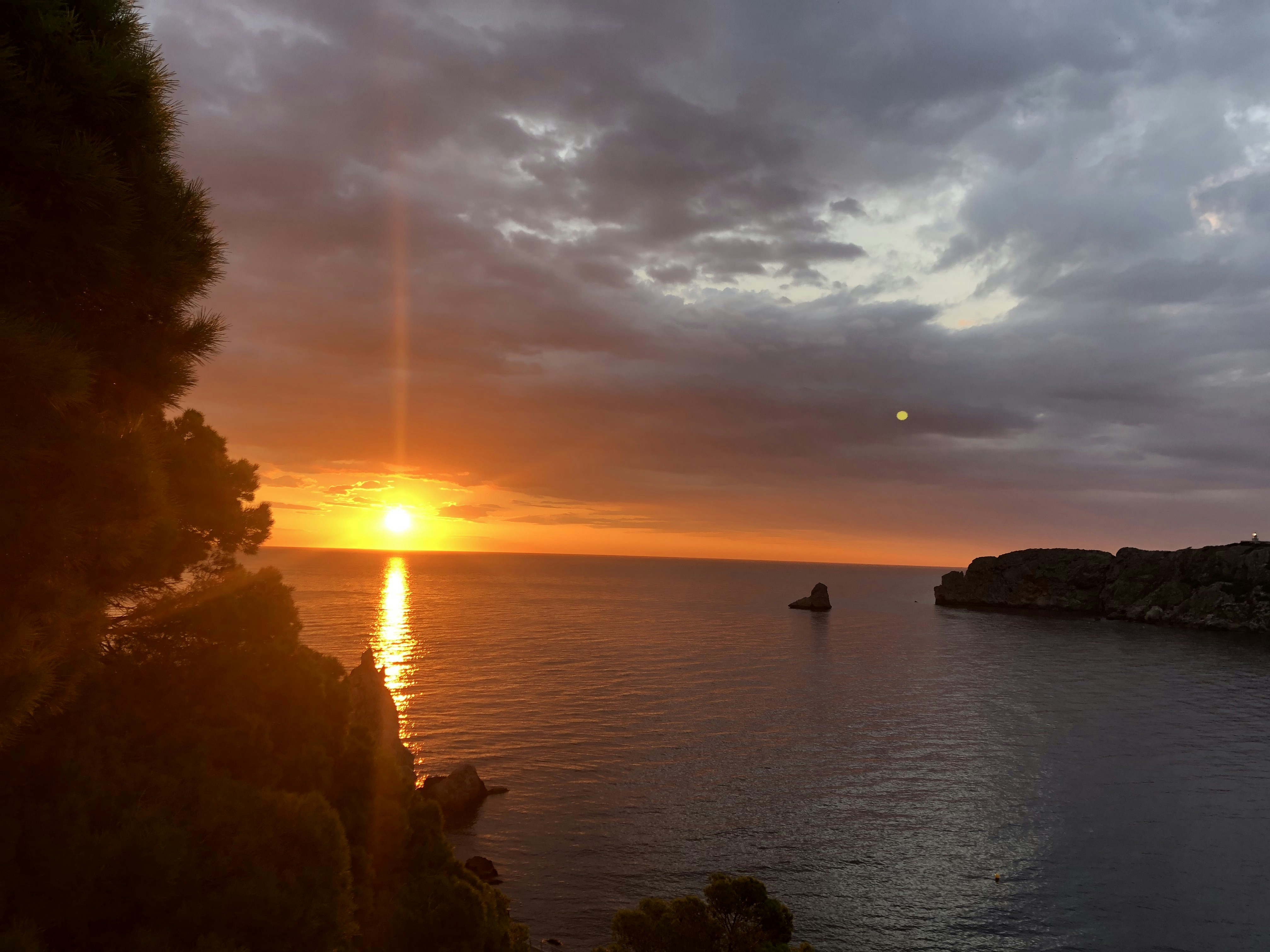 Sunset casting vibrant orange hues over a calm sea with silhouetted cliffs and clouds.