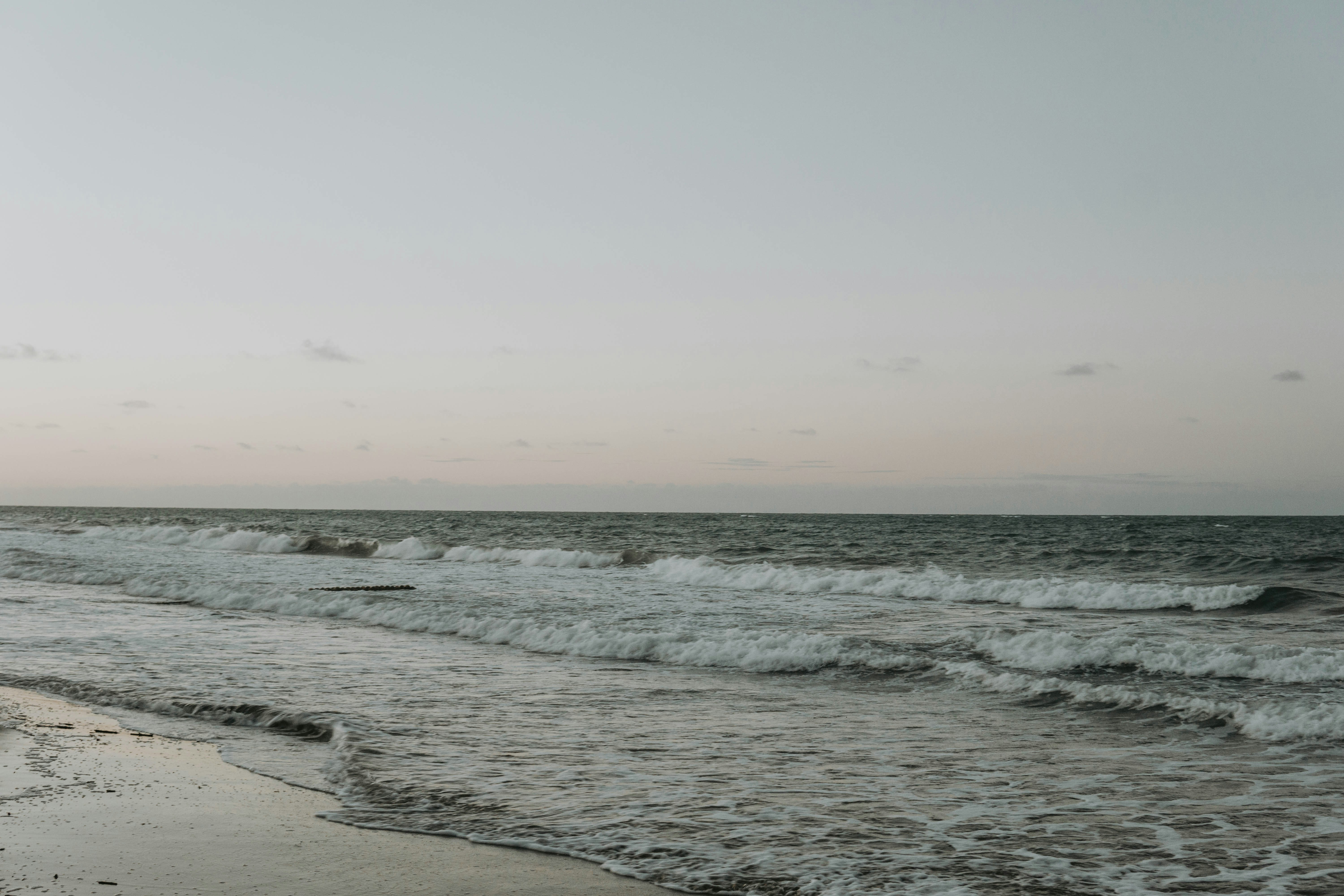 Gentle waves lapping at the shore under a soft dusk sky, creating a serene coastal atmosphere.