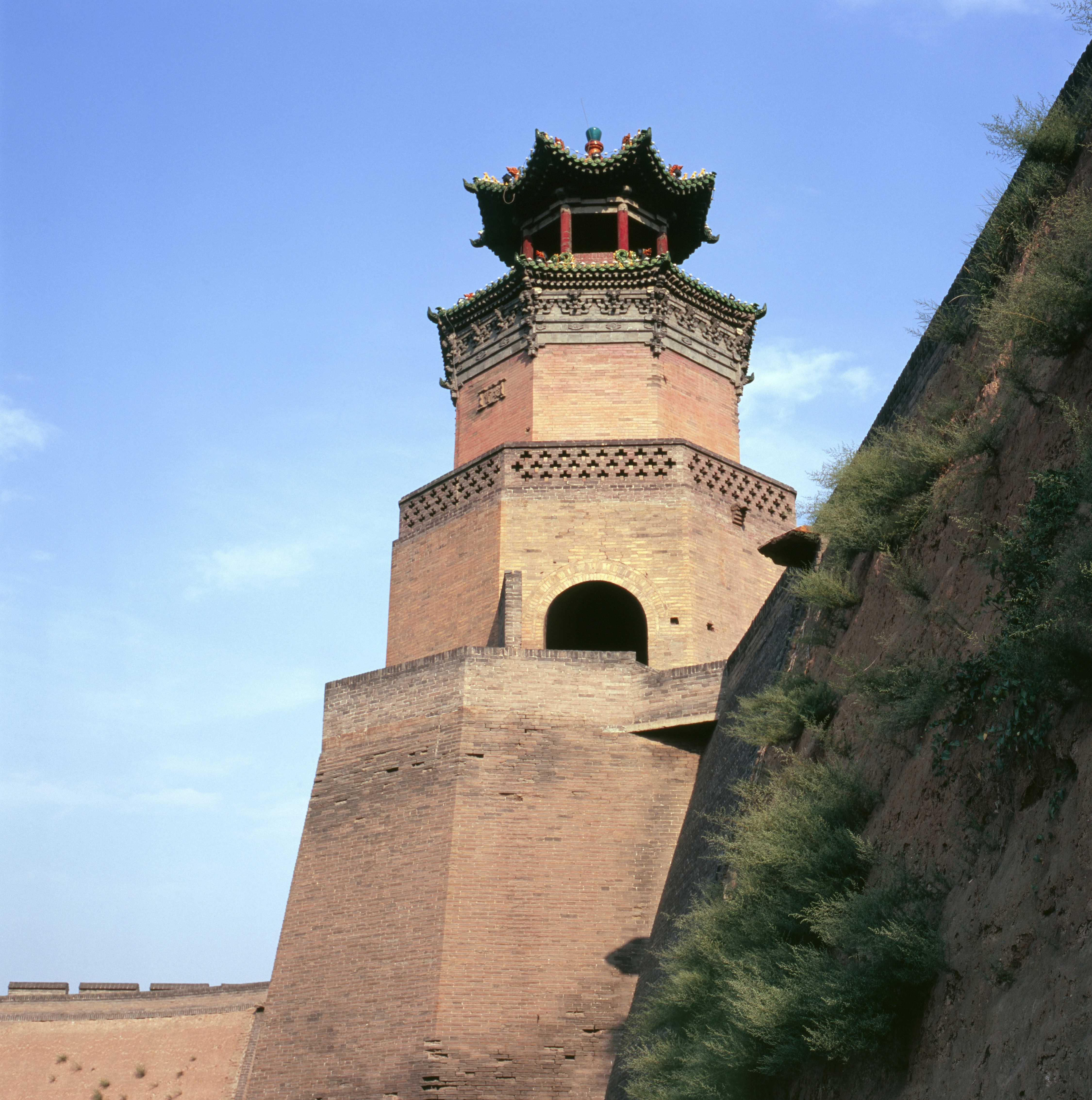 Historic watchtower rising from the ancient fortress wall, framed by a clear blue sky. The intricate architecture showcases traditional design elements.