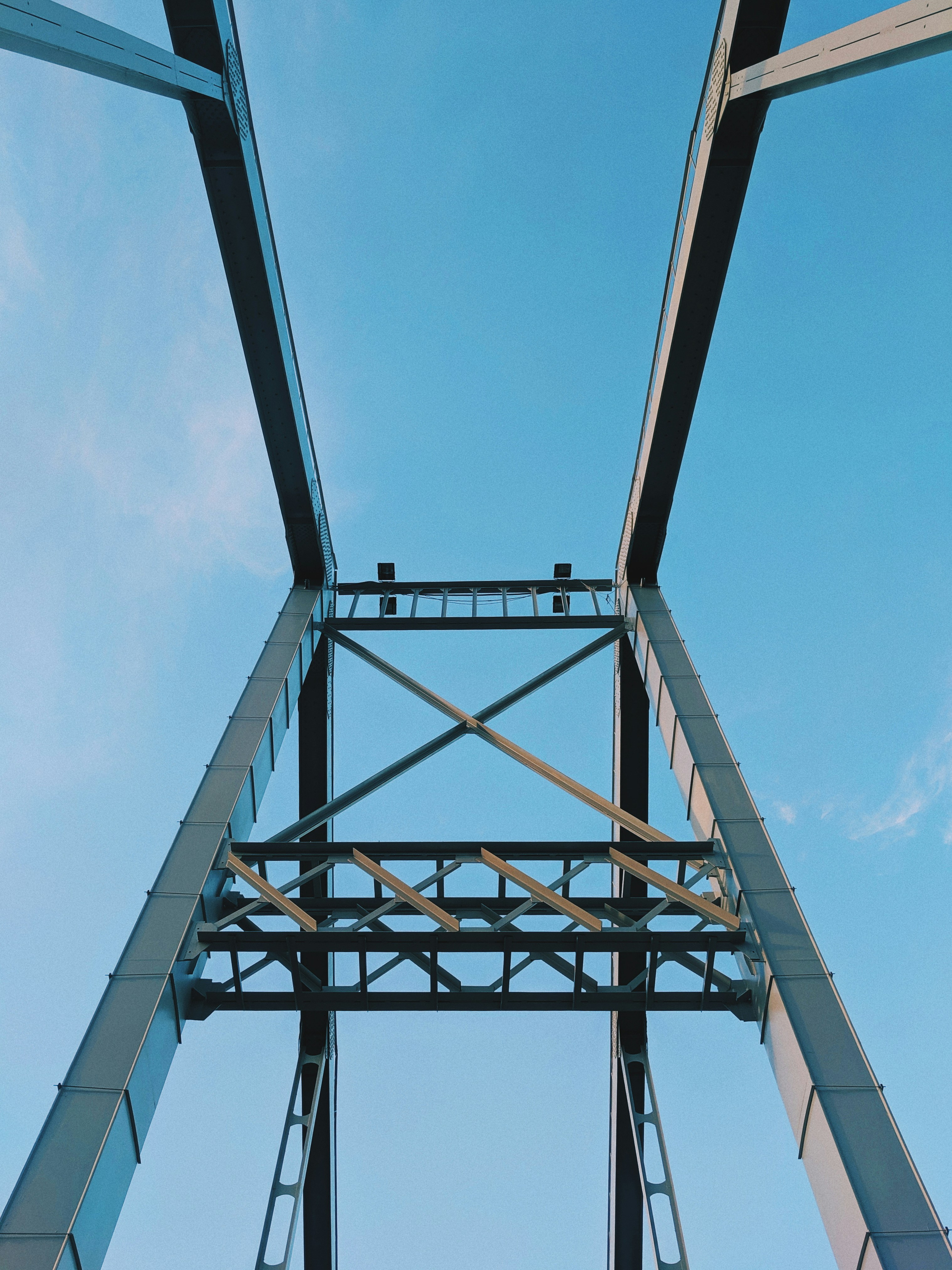 View from below a steel bridge, showcasing its intricate structure against a clear blue sky.