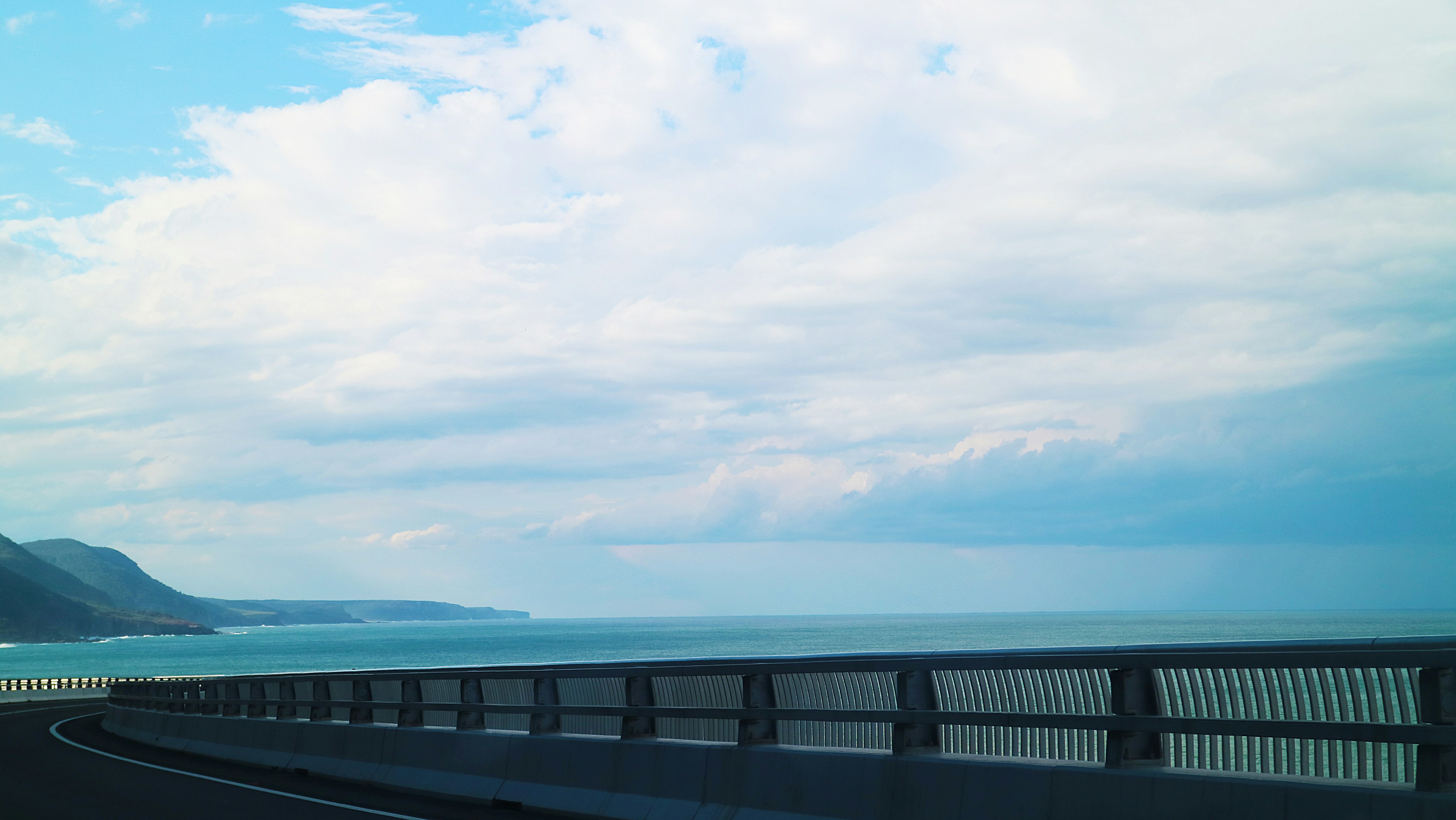 Winding coastal road alongside a tranquil sea under a cloudy sky, showcasing the harmony between land and water.