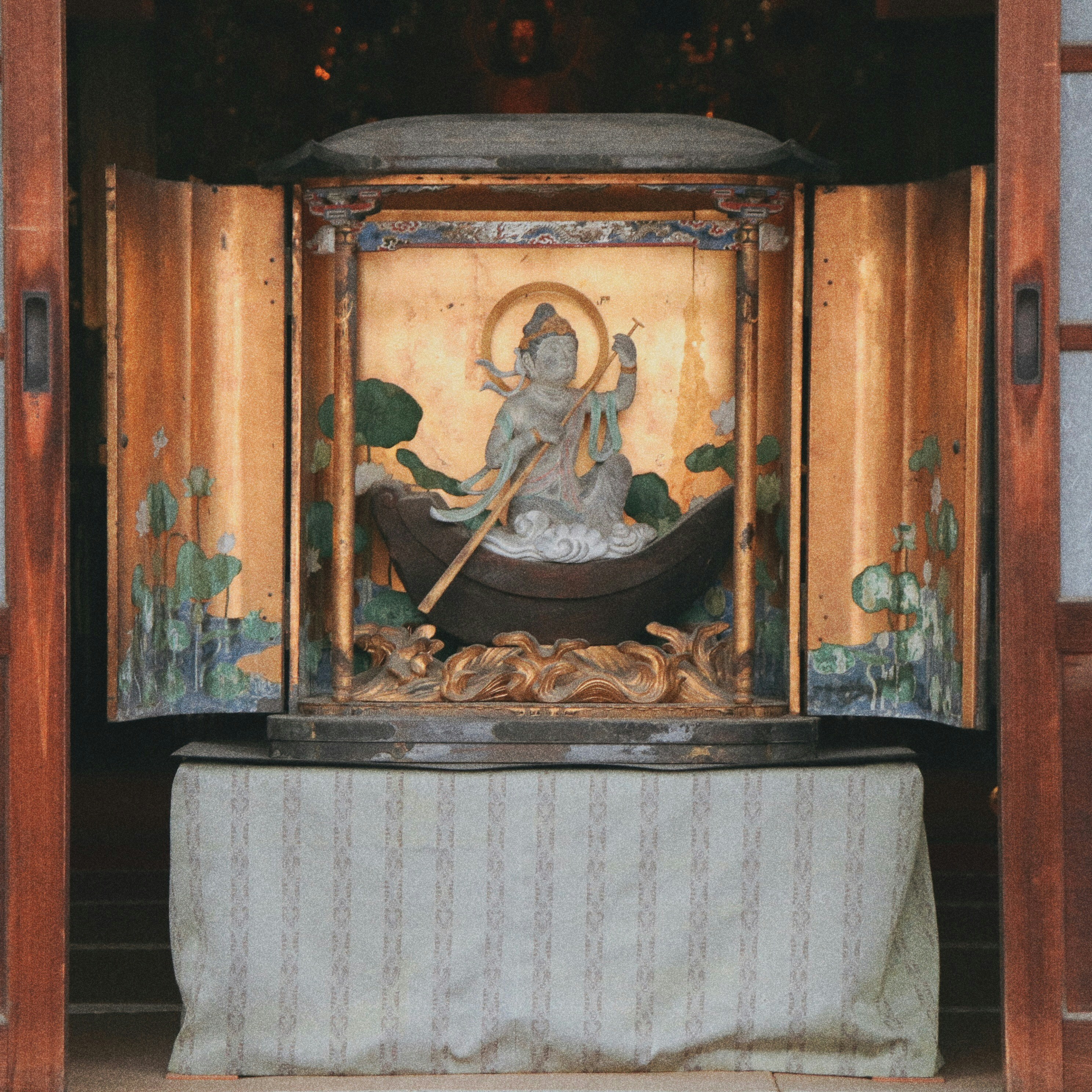 Intricately painted altar featuring a serene figure surrounded by lush greenery, framed by ornate wooden doors. The artwork embodies tranquility and spiritual significance.