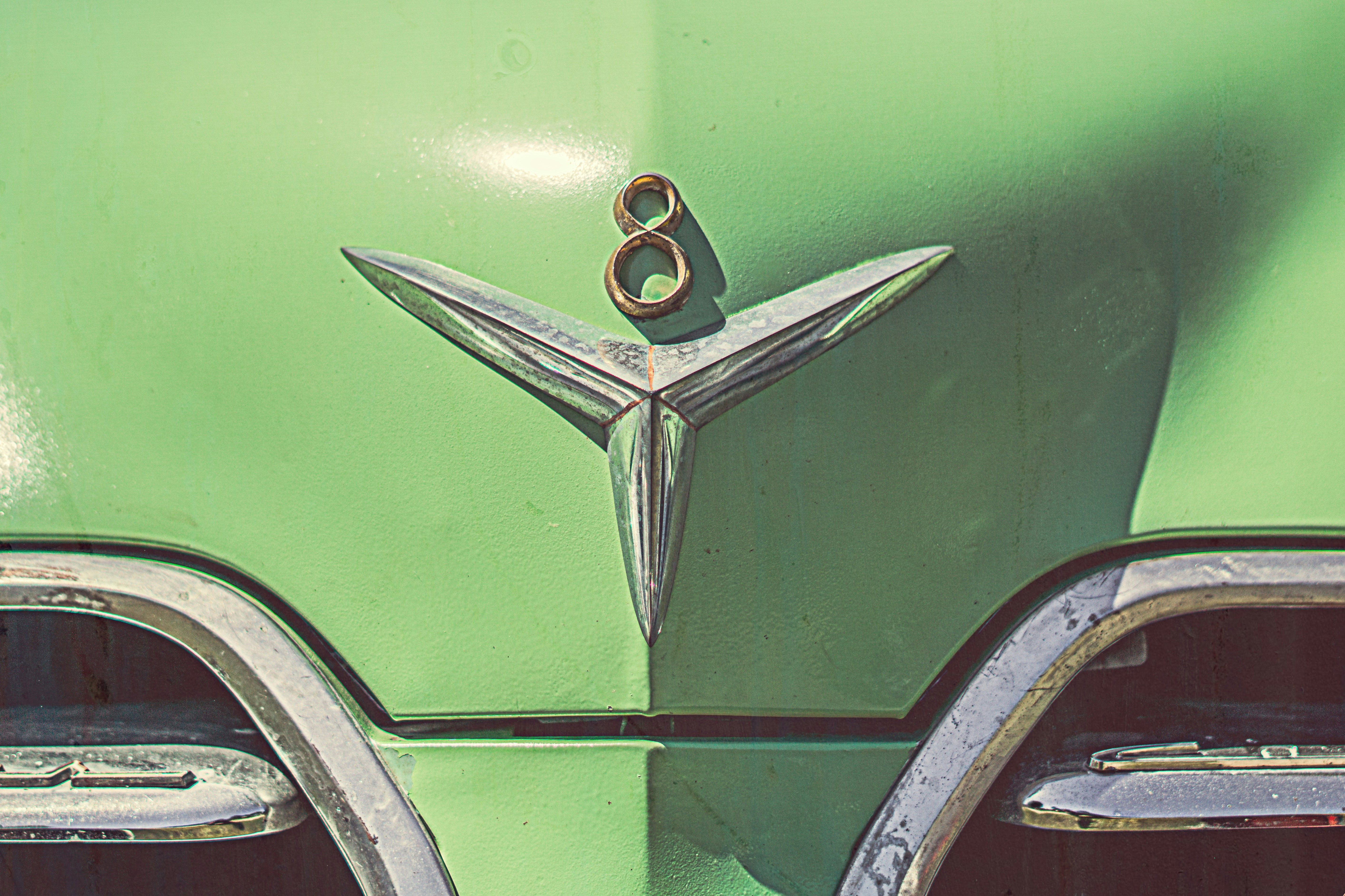 Close-up of a vintage car's hood ornament featuring an '8' emblem, set against a textured green background.
