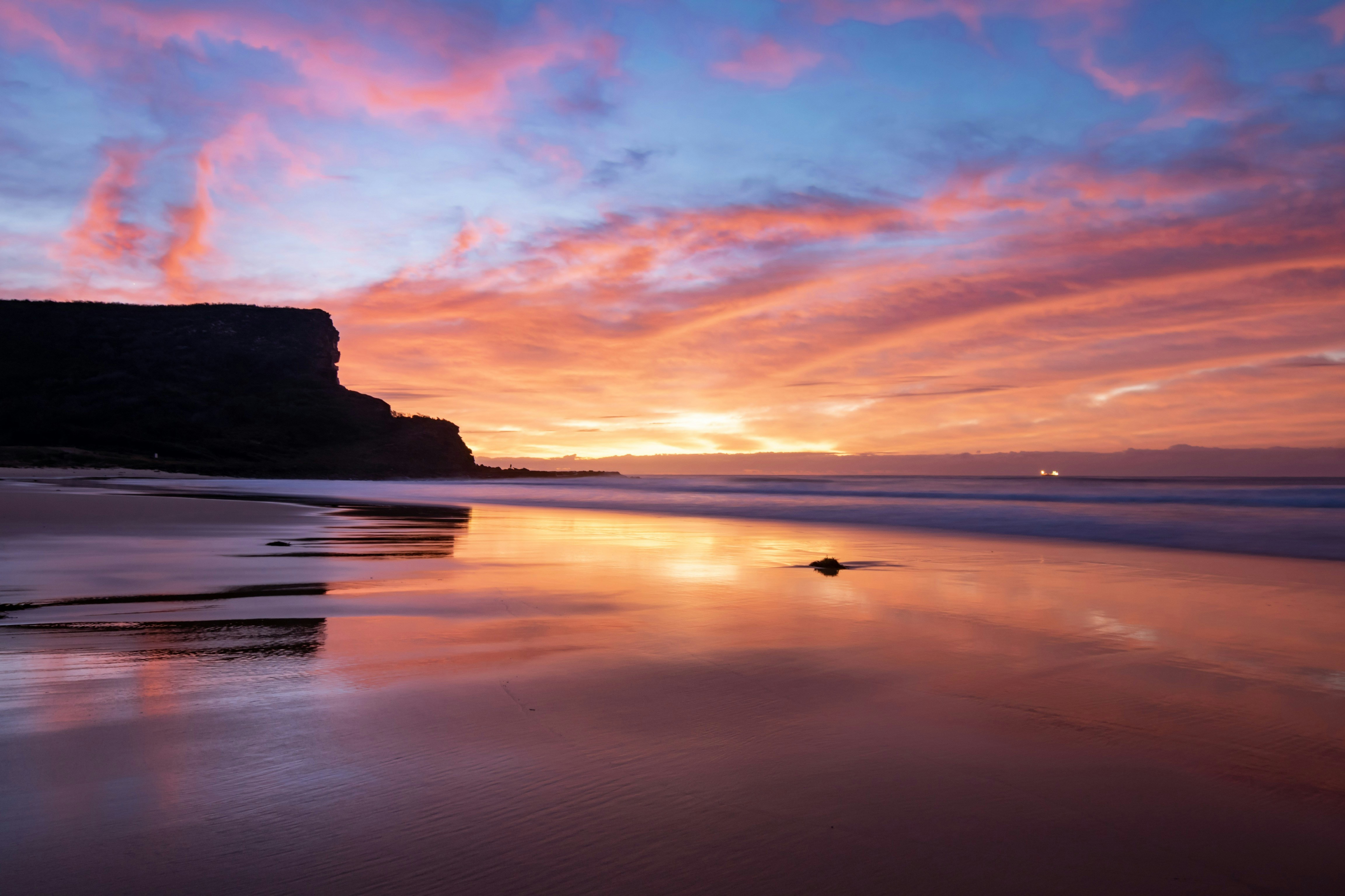 Horizon Fire over a Glassy Shore: Sunset Reflections by the Cliff