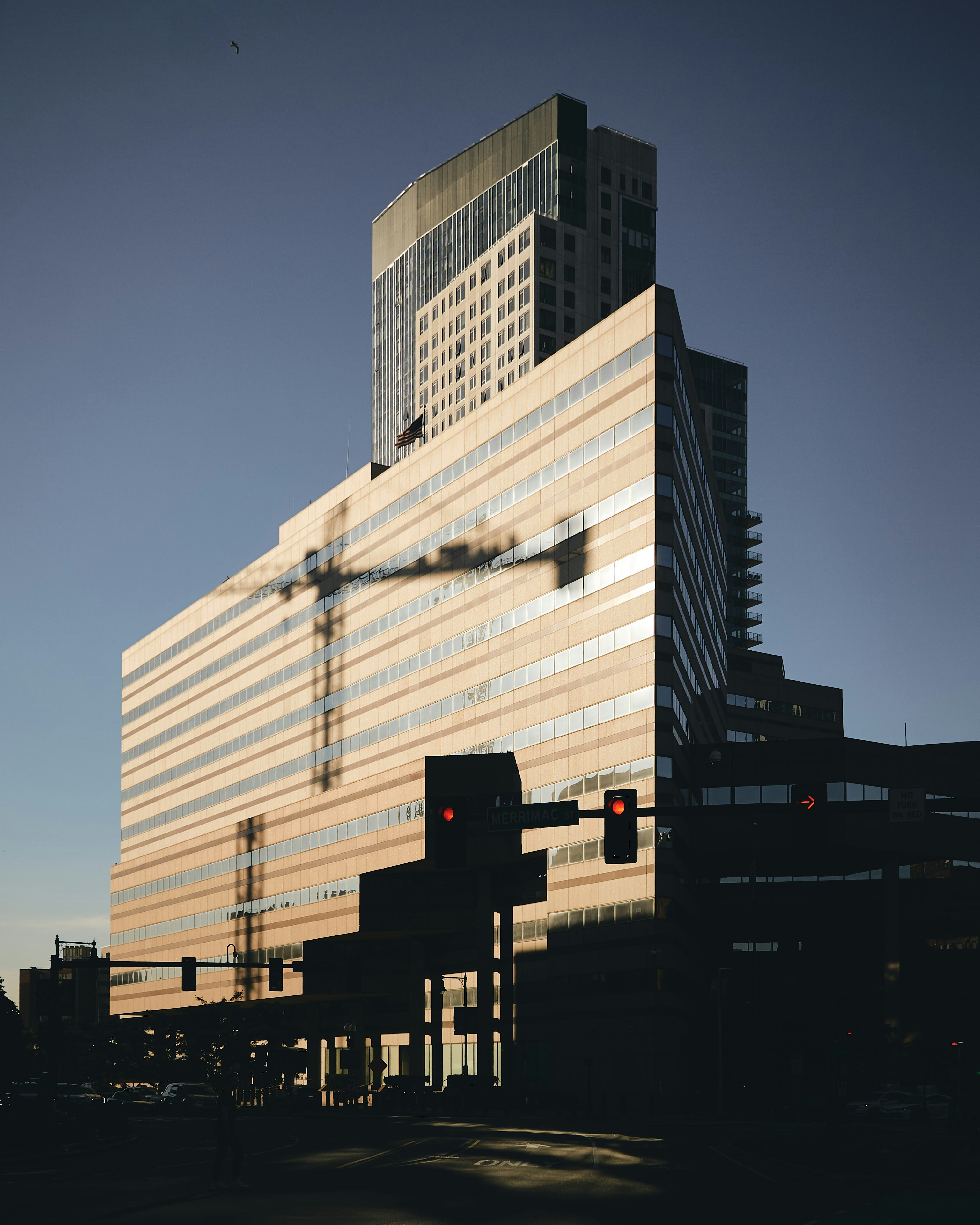 A modern skyscraper reflecting warm tones during sunset, with distinct shadows cast by a nearby traffic light and construction crane.