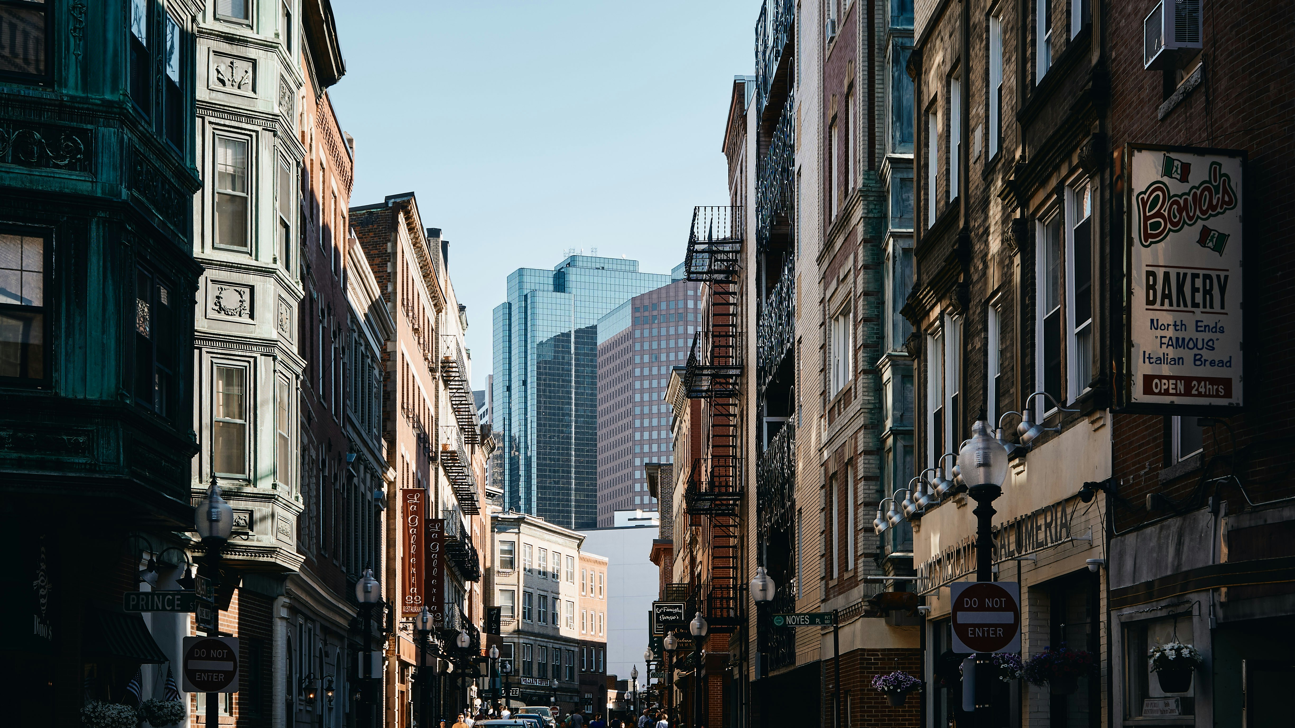 Narrow city street flanked by historic buildings leading to modern skyscrapers under a clear blue sky.