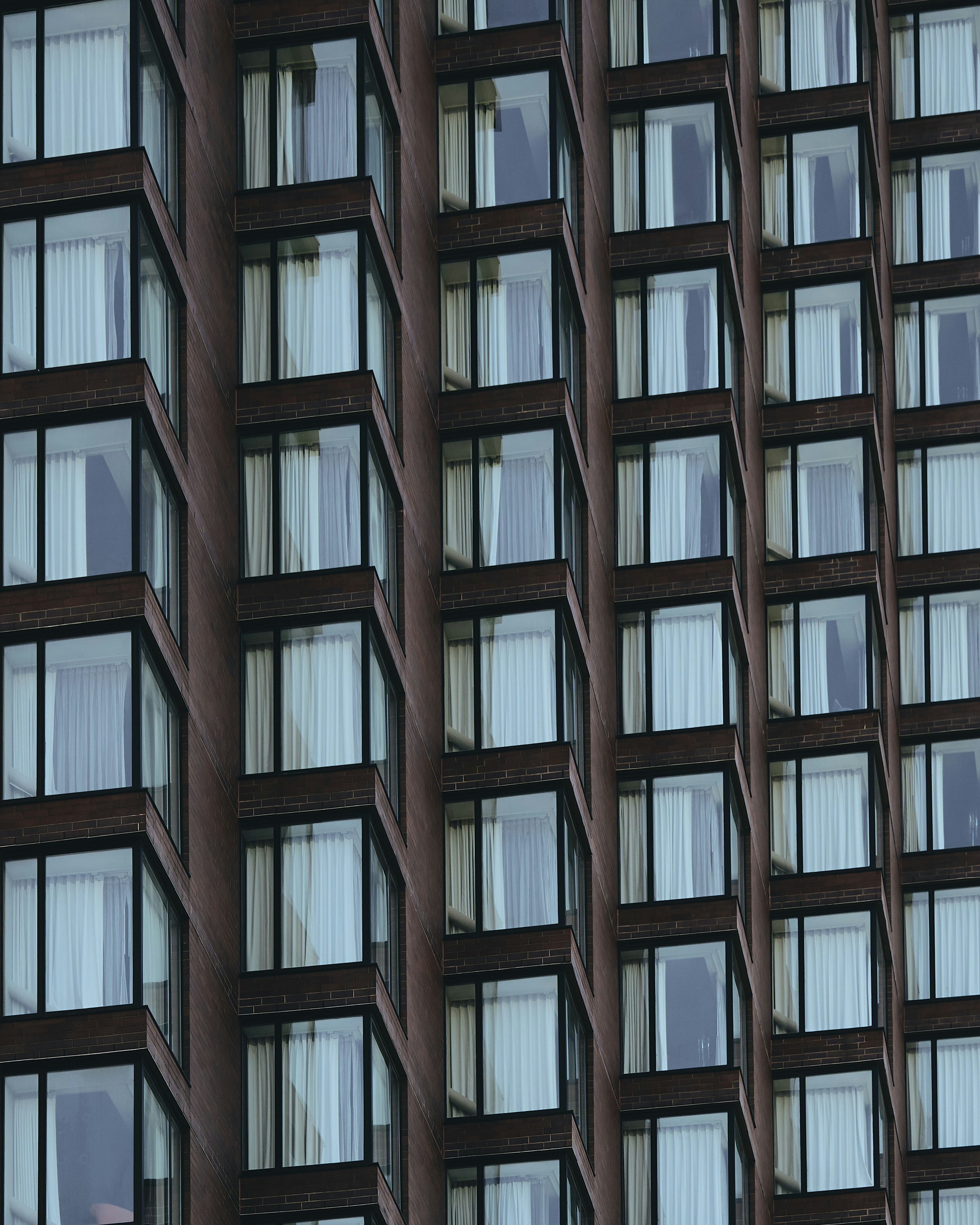 Close-up of a modern building's facade showcasing a repetitive pattern of windows with sheer curtains.