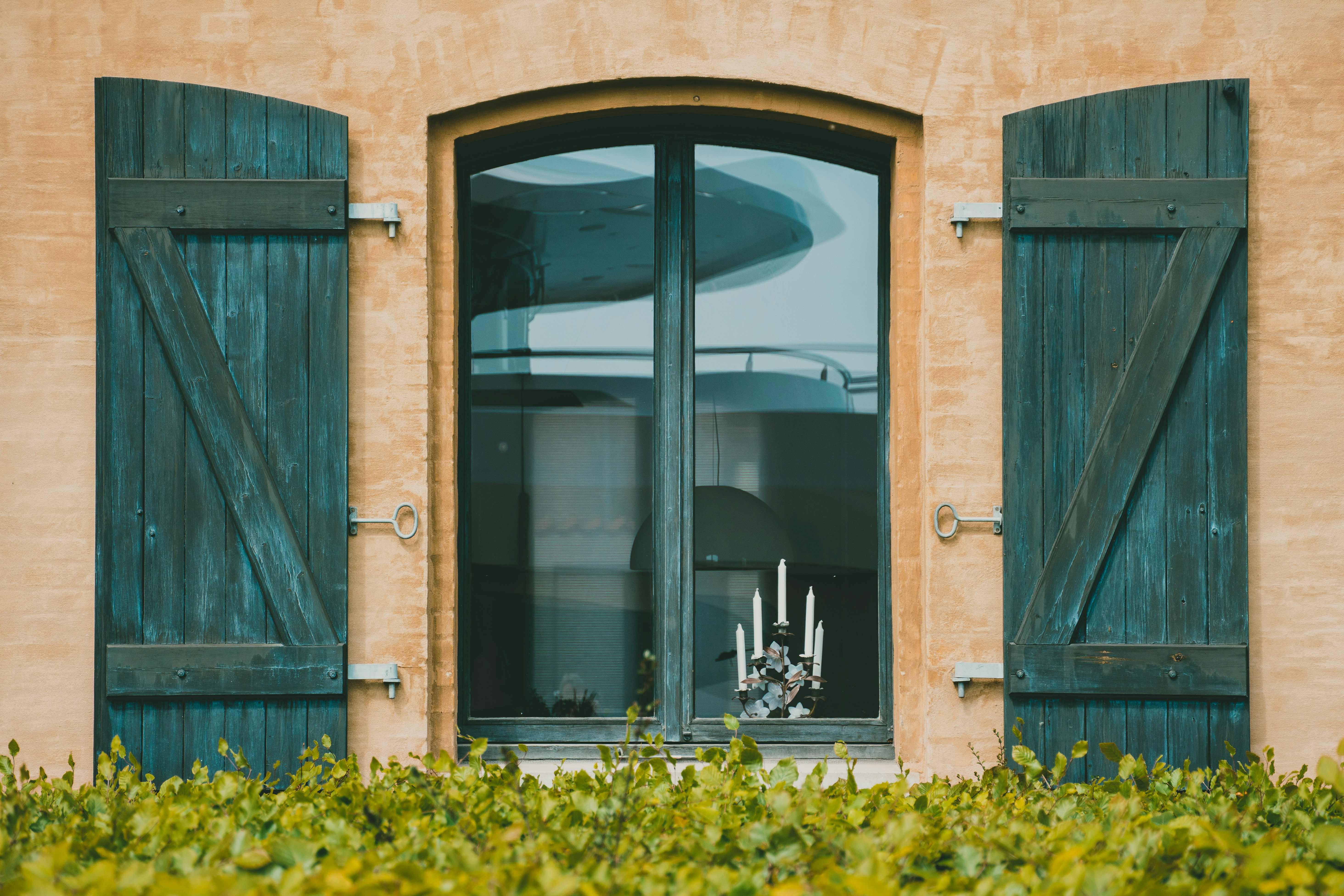 Arched Window Between Teal Shutters on a Sunlit Ochre Facade
