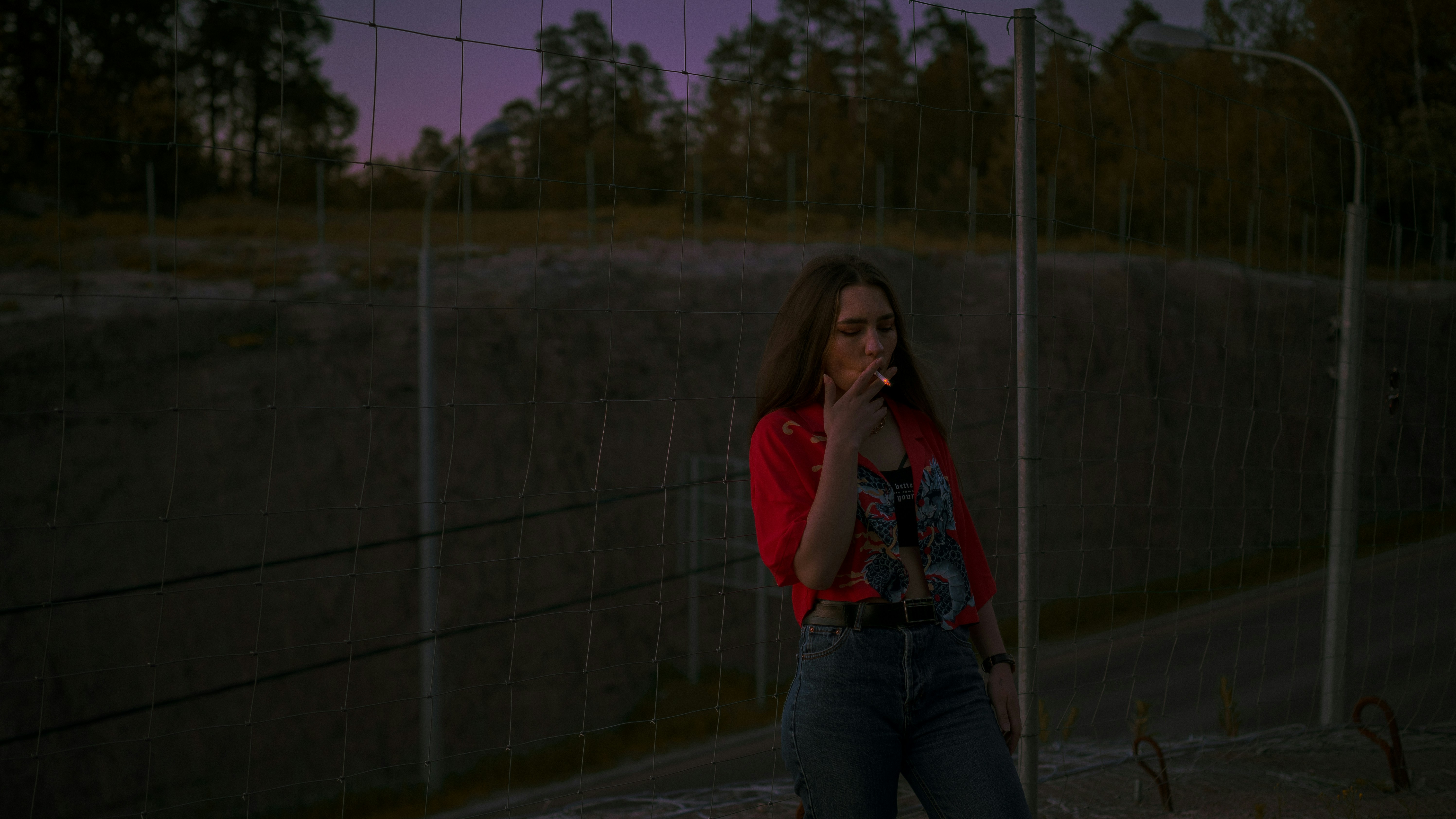 Evening Edge: a cigarette and red jacket in a fence-lined dusk