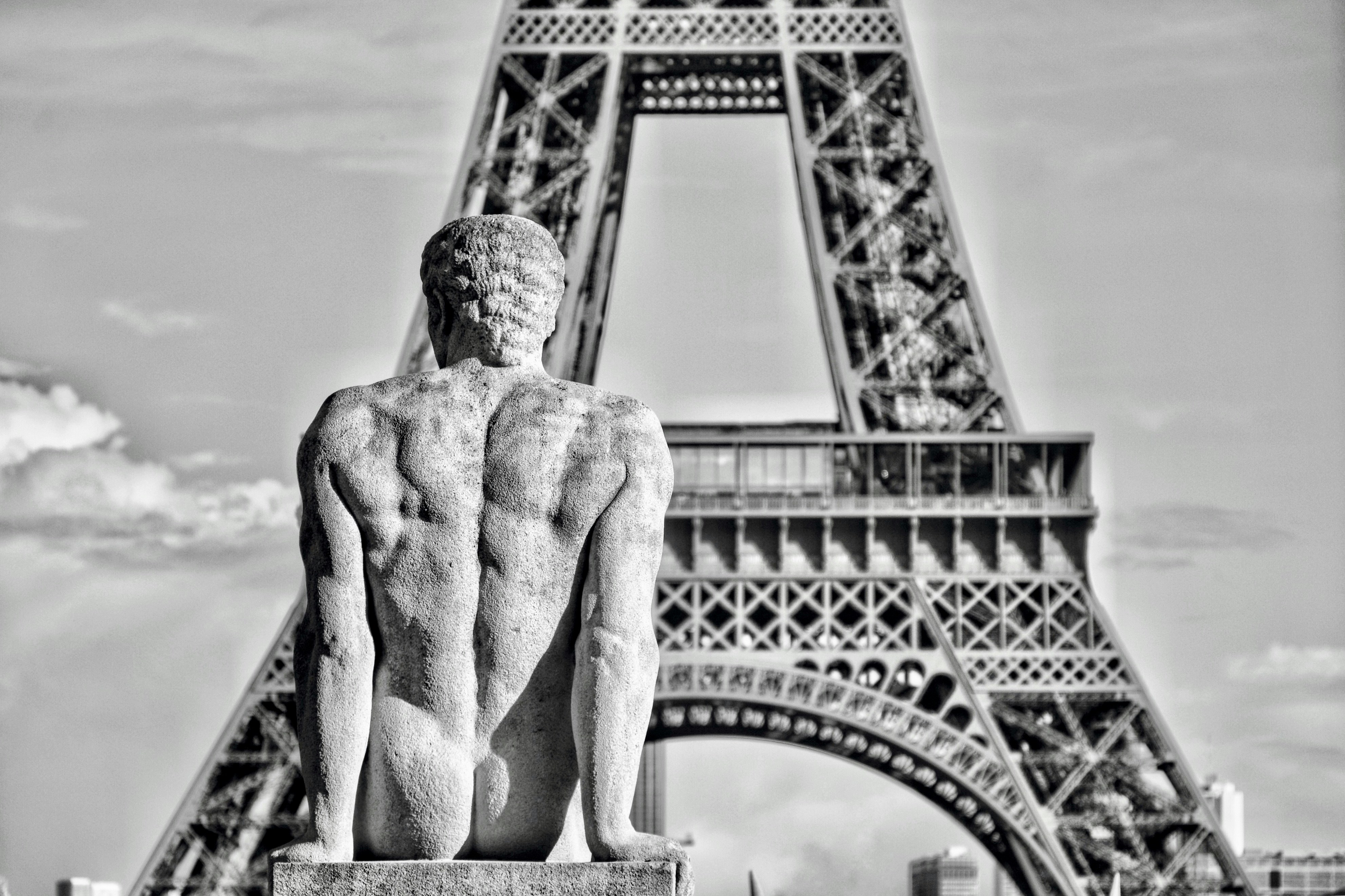 A sculpted figure gazes towards the Eiffel Tower, embodying a moment of reflection against a monochromatic backdrop.