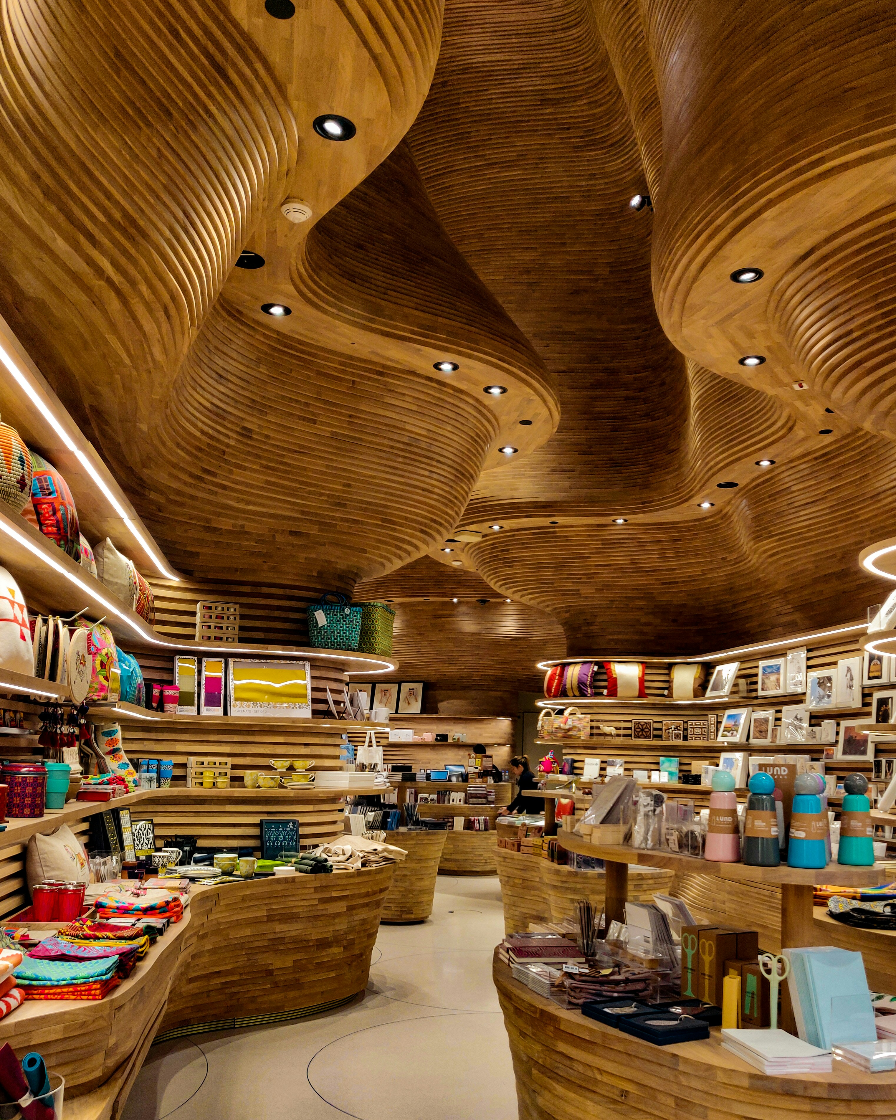 Interior of a uniquely designed store featuring curved wooden shelves filled with colorful merchandise and ambient lighting.