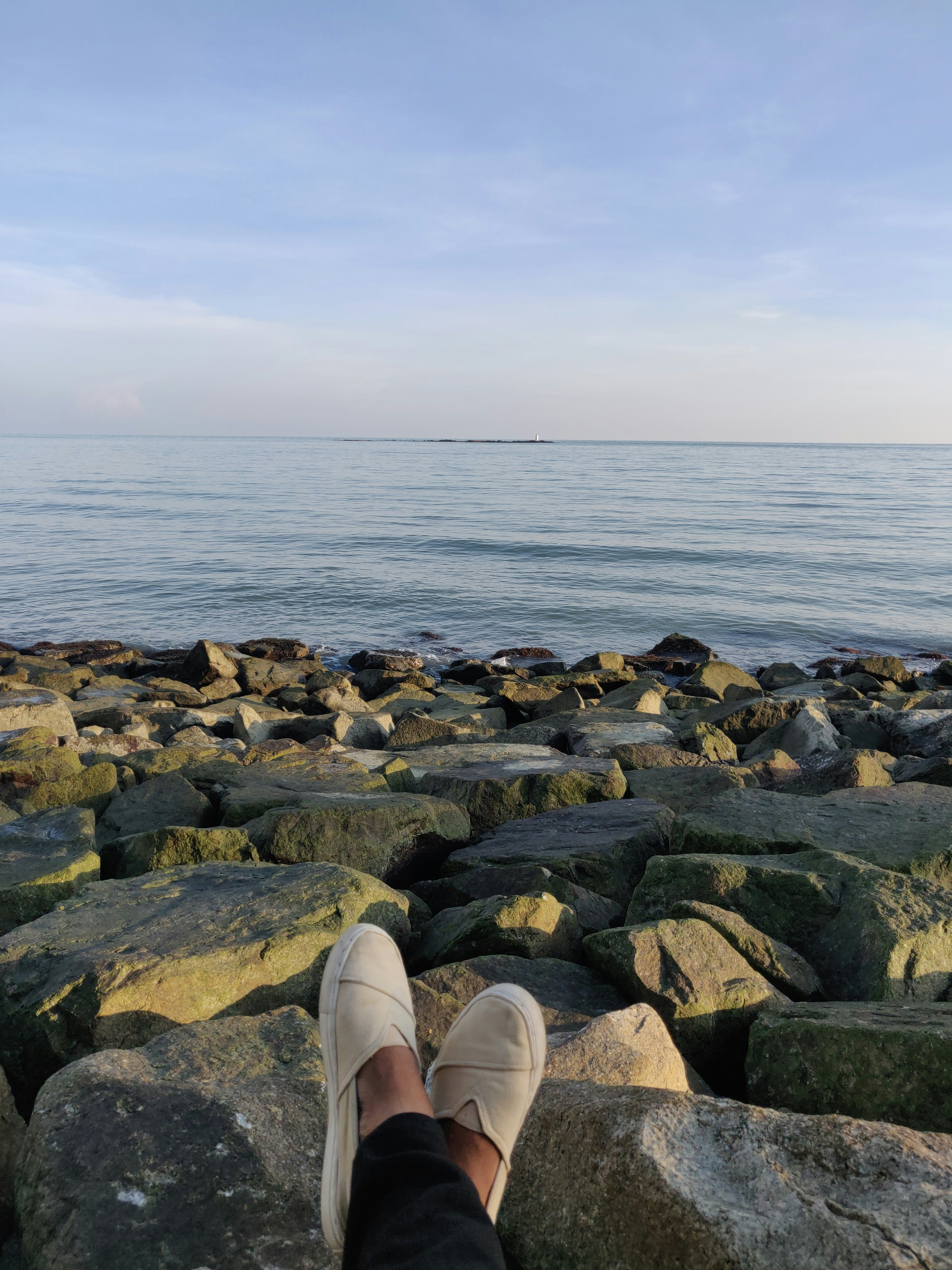 Feet resting on rocky shoreline with calm waters stretching to the horizon under a clear sky.