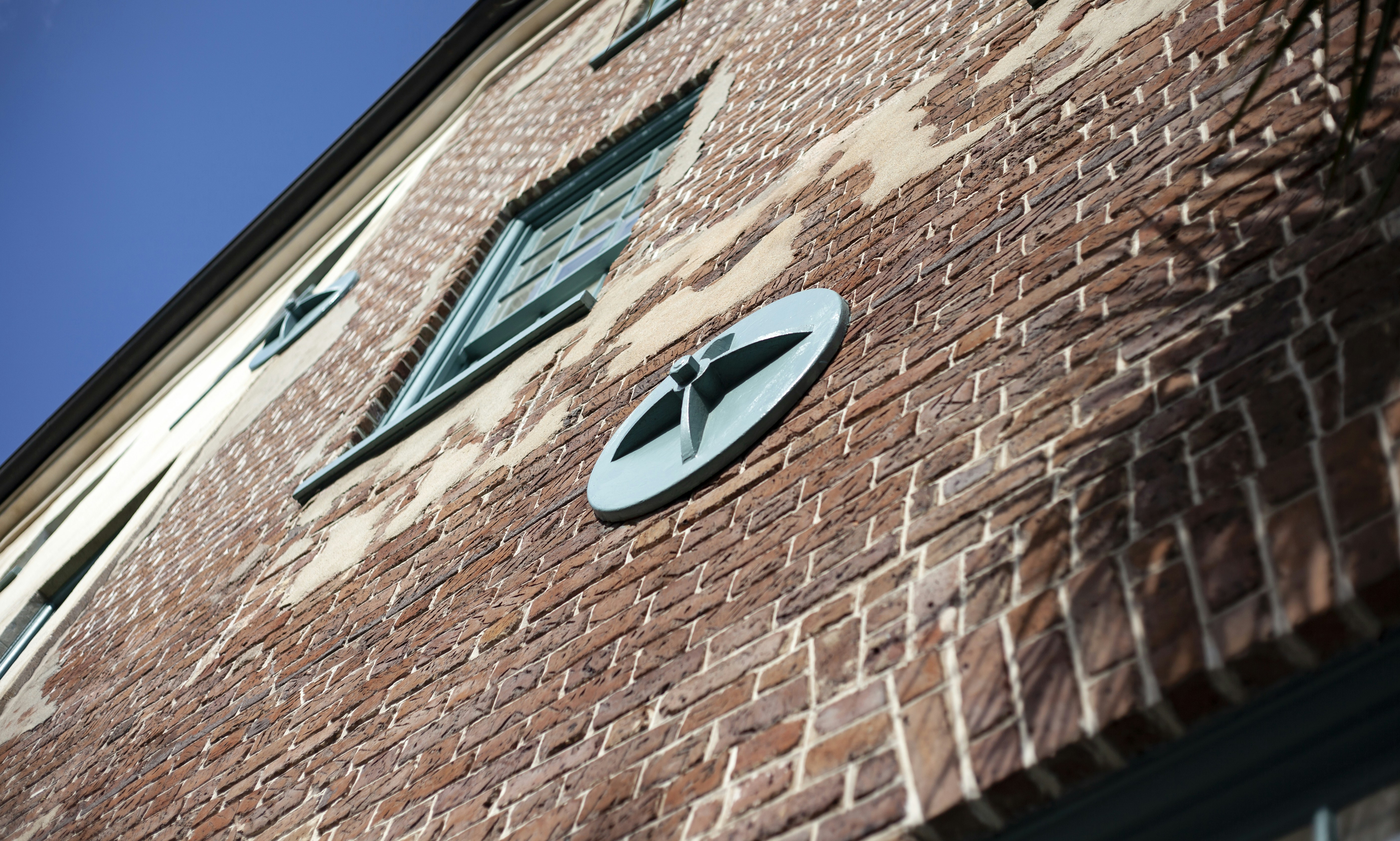 Blue metal plate on brick wall under clear sky, originally an earthquake bolt.