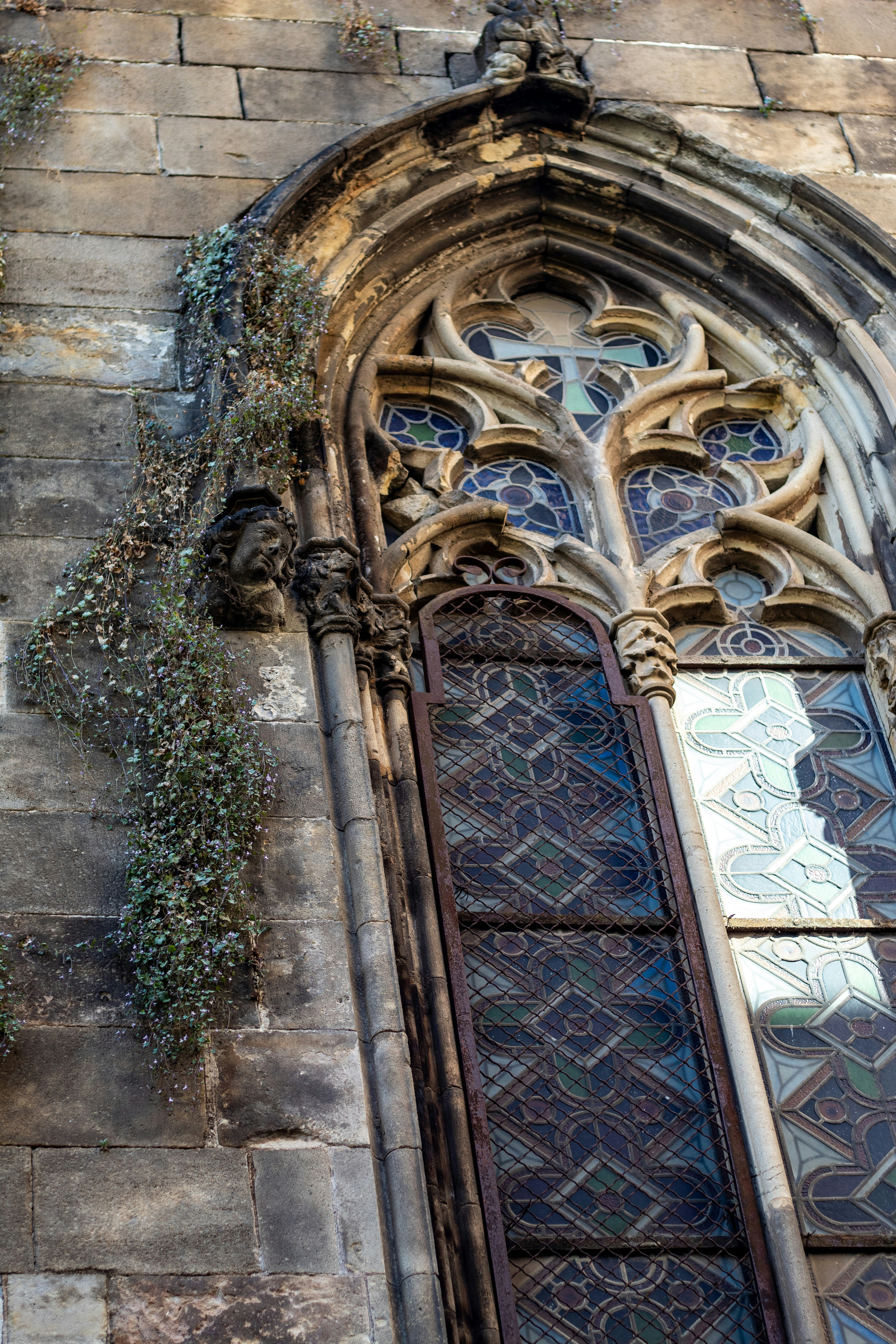 Intricate Gothic window adorned with elaborate stonework and creeping ivy, showcasing the interplay between nature and architectural artistry.
