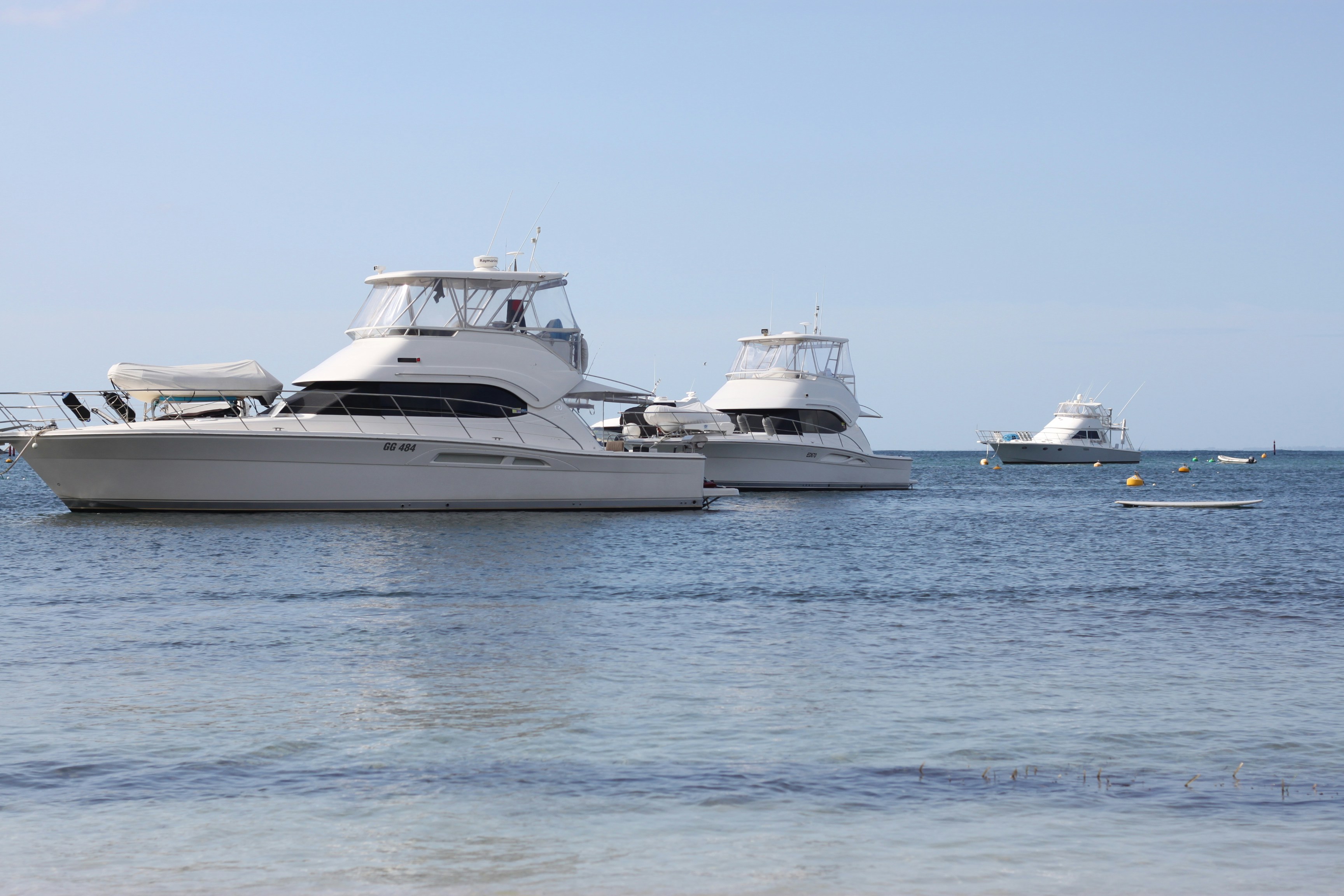 Three luxurious yachts anchored in calm waters under a clear sky. The scene conveys a tranquil maritime atmosphere.