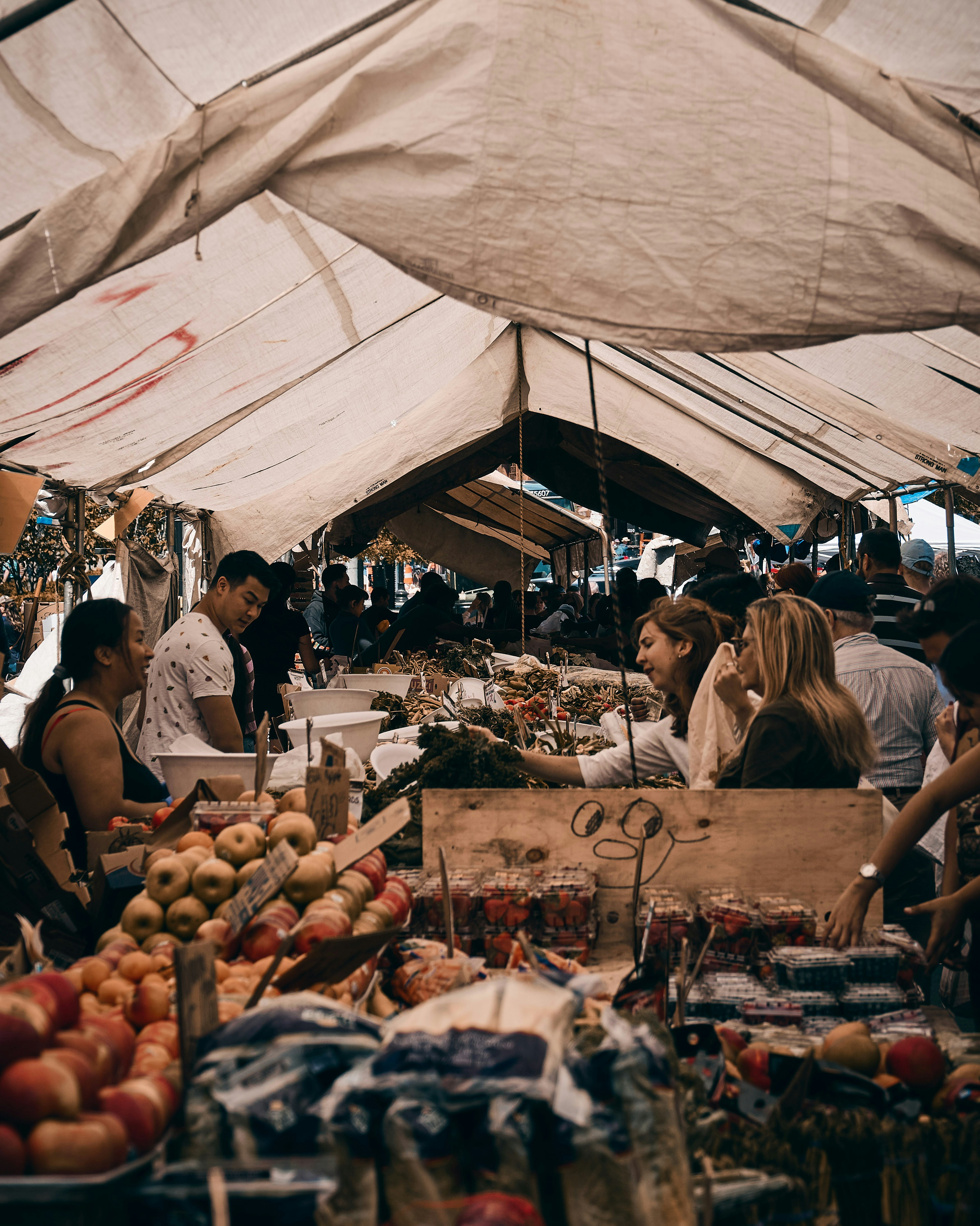 Vibrant market scene with stalls overflowing with fresh produce and bustling shoppers engaged in lively conversation.