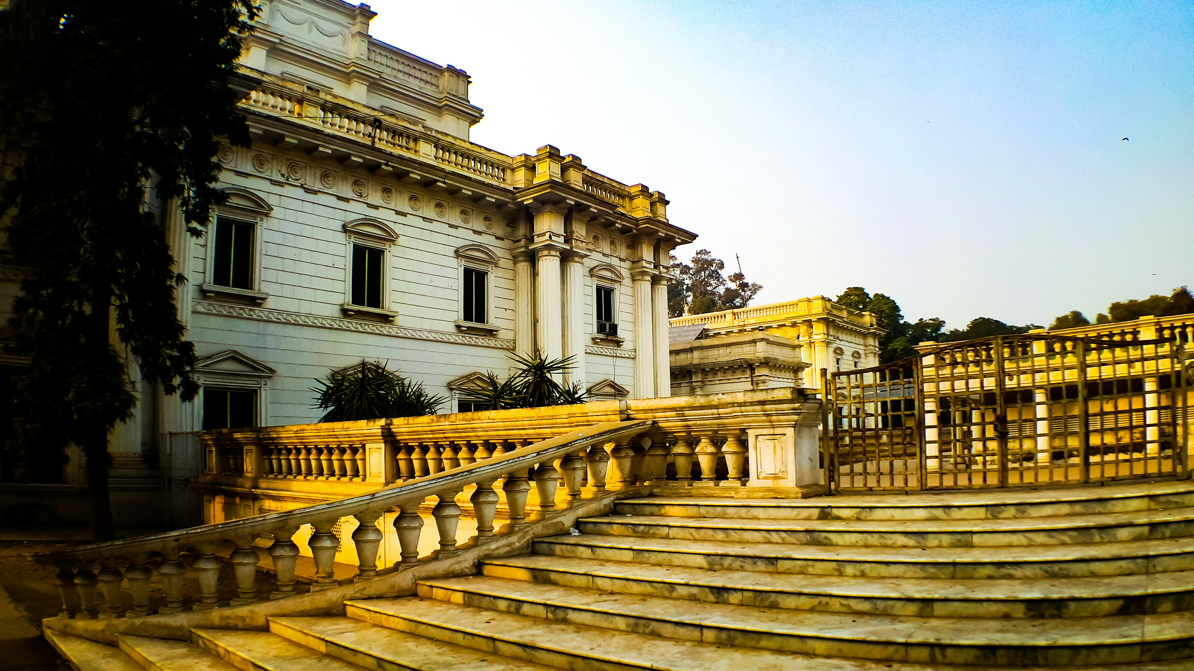 Historic neoclassical estate bathed in warm sunset light, with sweeping stone steps and ornate balustrades leading to a stately façade.