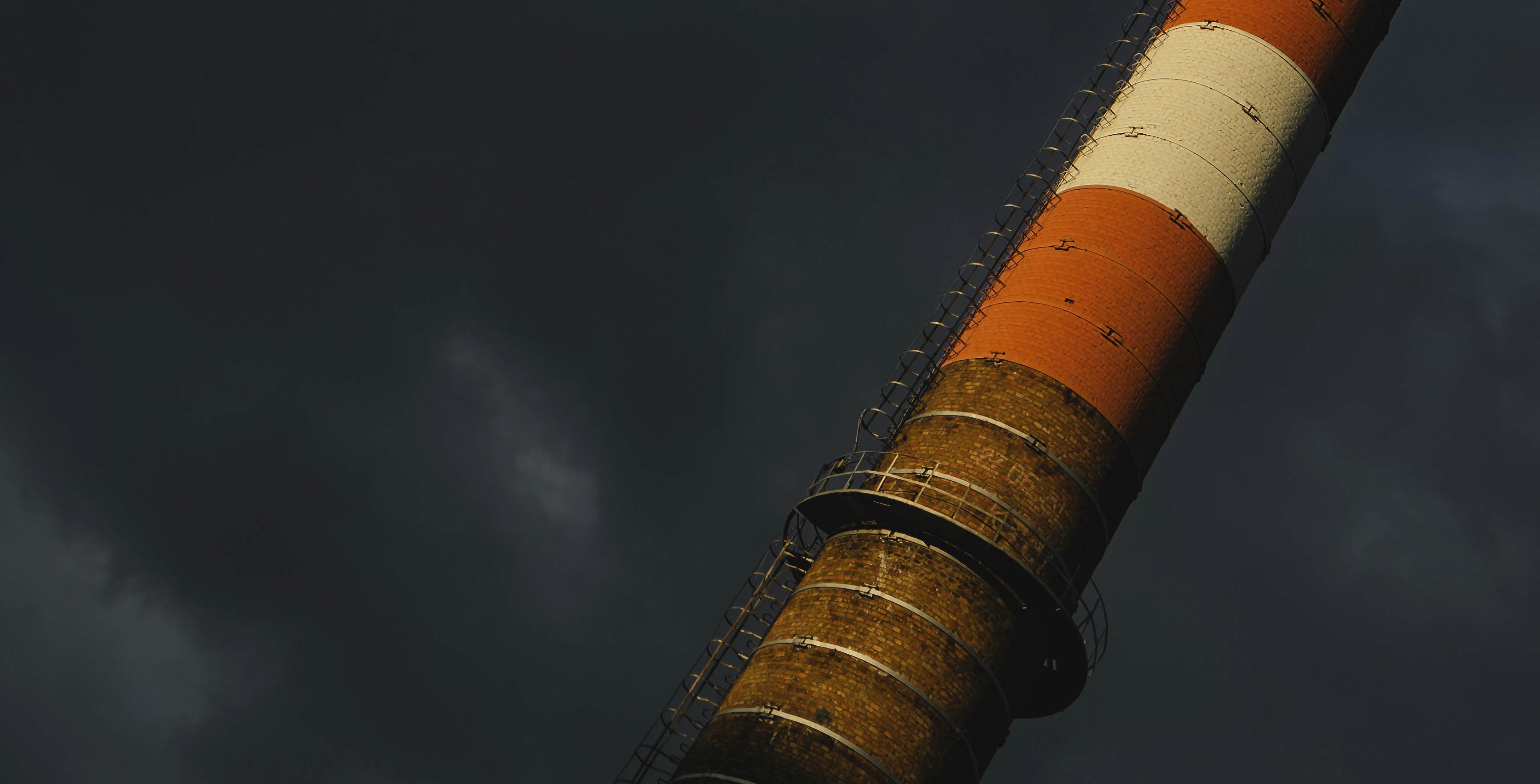 A towering smokestack against a moody sky, showcasing the industrial landscape's starkness and the interplay of light and shadow.