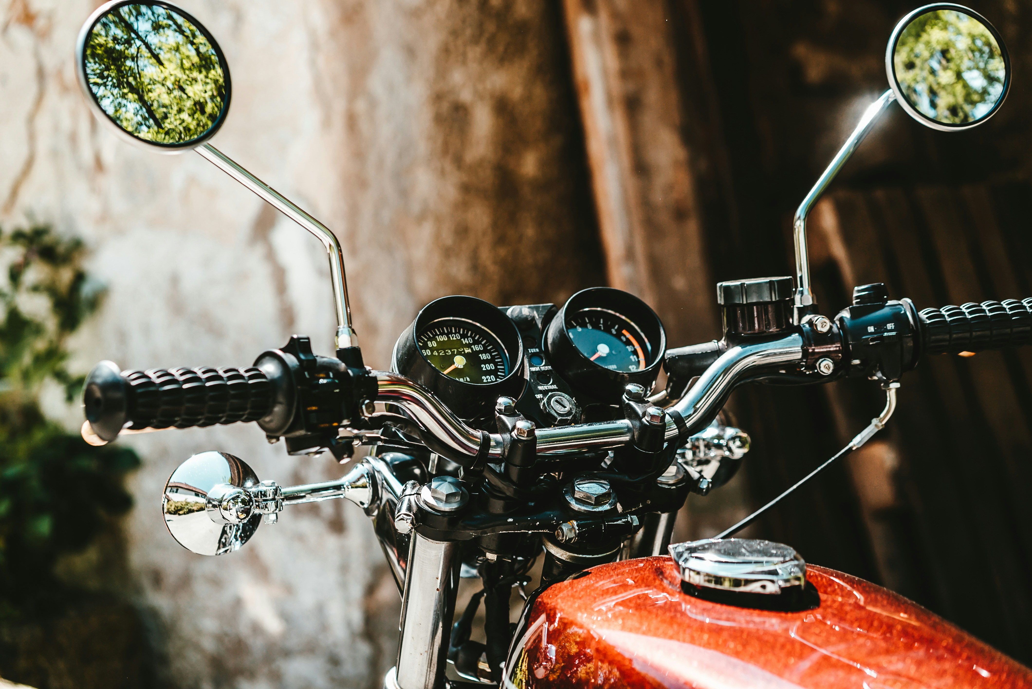 Close-up of a classic motorcycle's handlebars and gauges against a rustic backdrop.