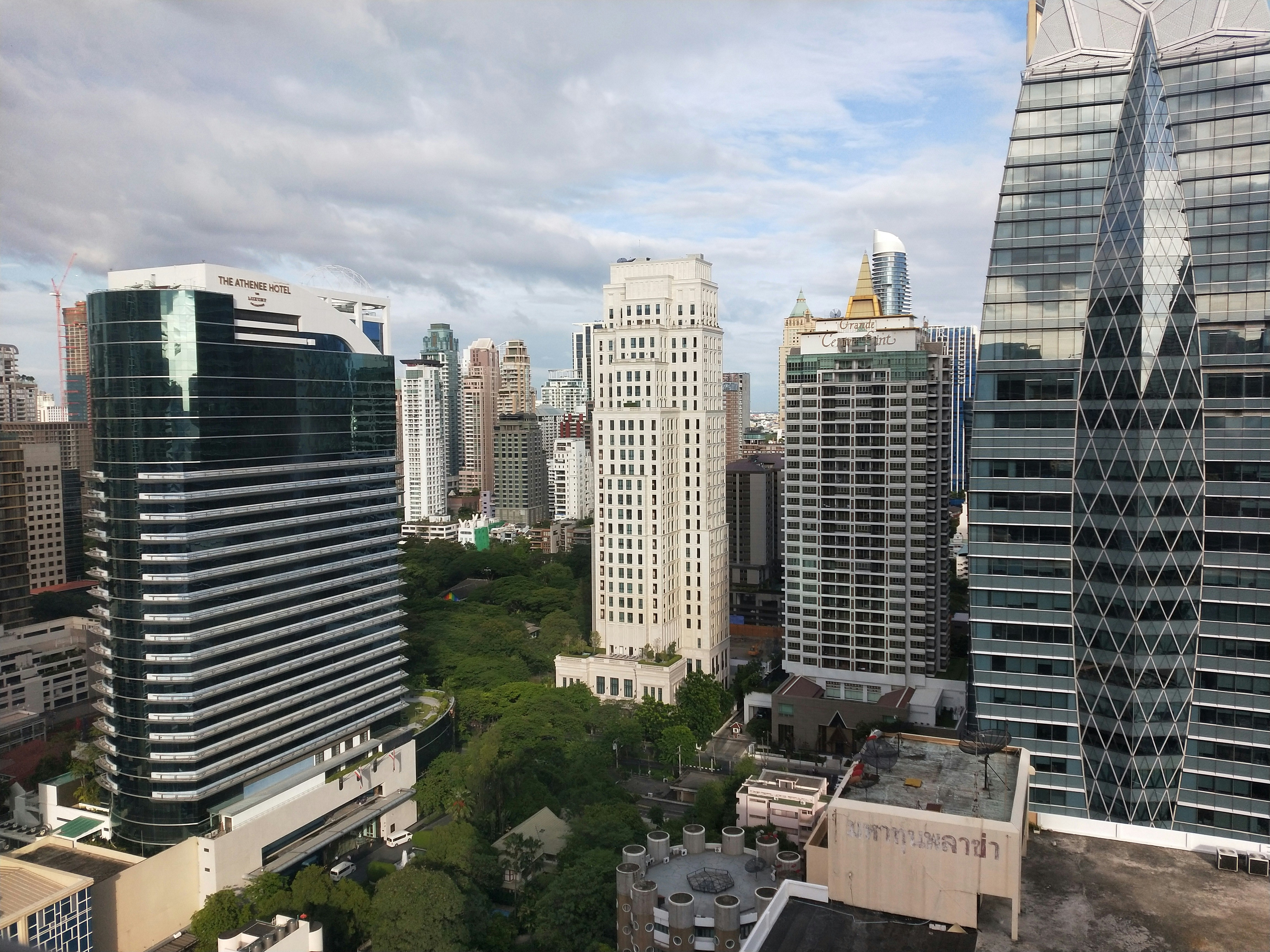 High-rise buildings surround a green park under a partly cloudy sky.