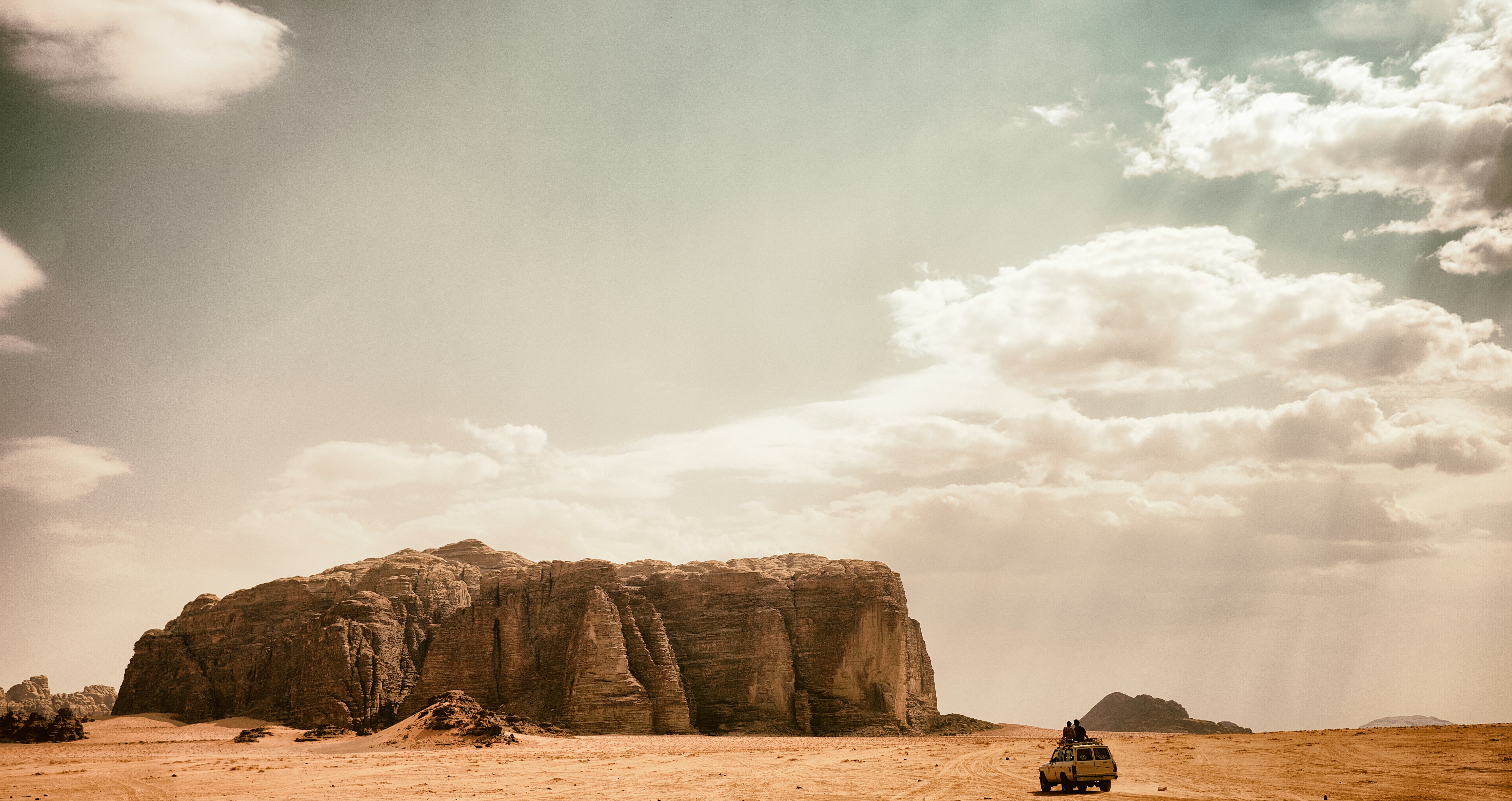 A rugged vehicle traversing the vast desert landscape, framed by imposing rock formations and a dramatic sky.