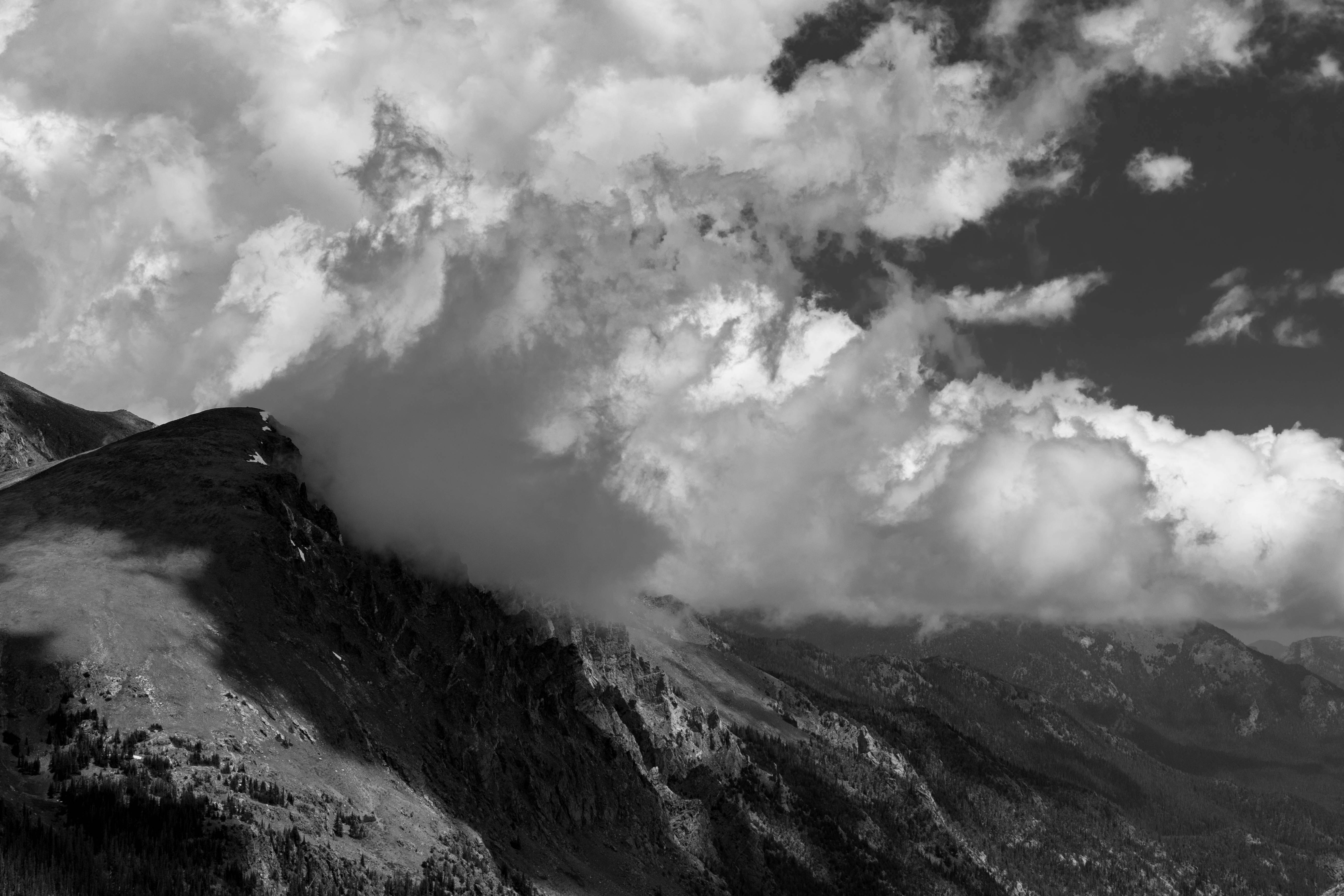 Dramatic mountain landscape enveloped by swirling clouds, showcasing the interplay of light and shadow in a monochrome palette.